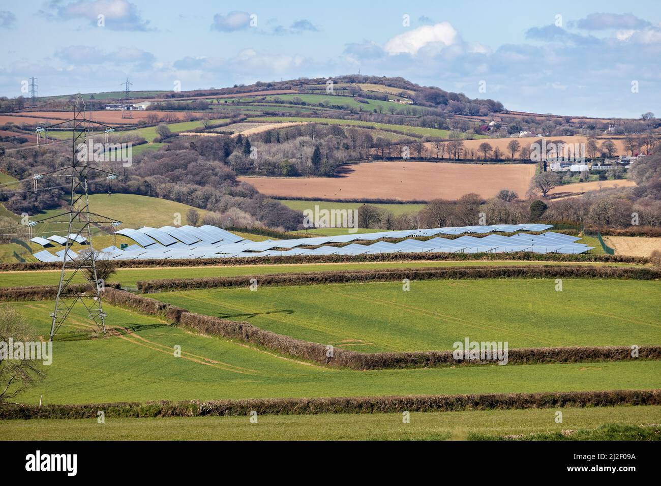 A solar farm and electric pylons pictured in the green fields of ...