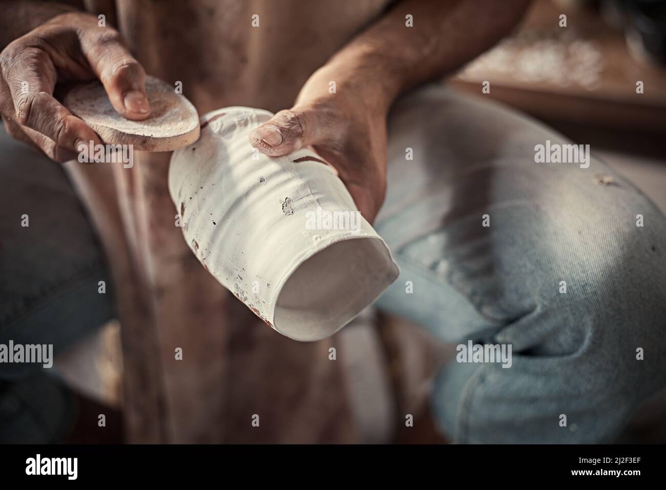 the artist polishing rough edges of a ceramic pot with a sponge in ...