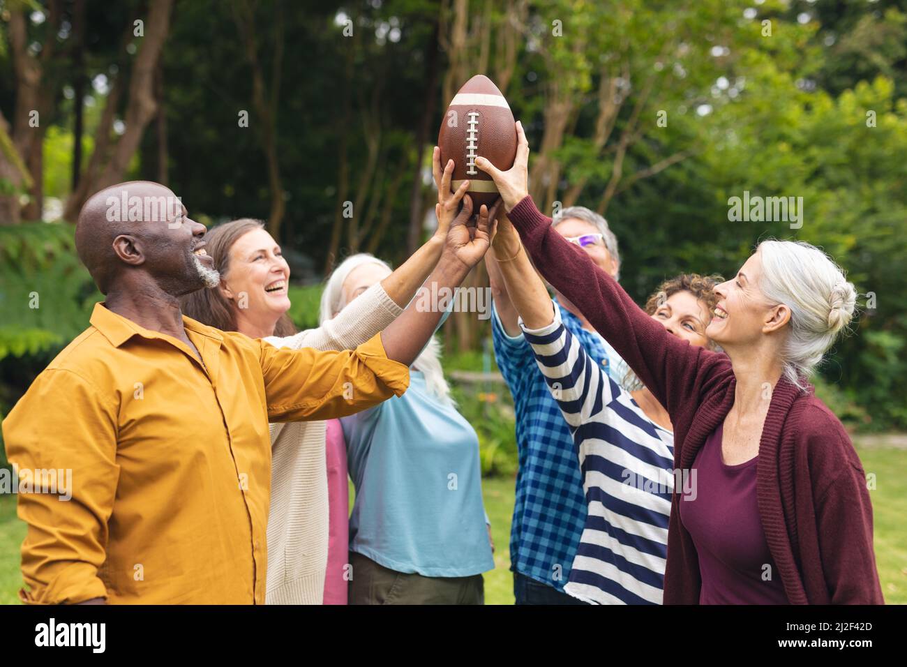 Happy multiracial active senior male and female friends holding rugby ...