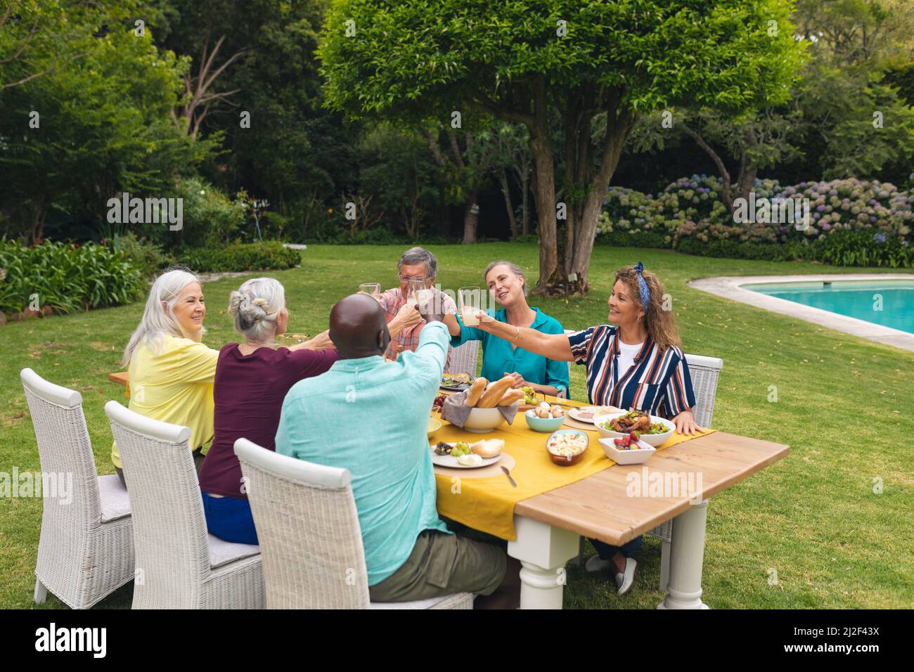 Multiracial senior male and female friends toasting wine at table ...