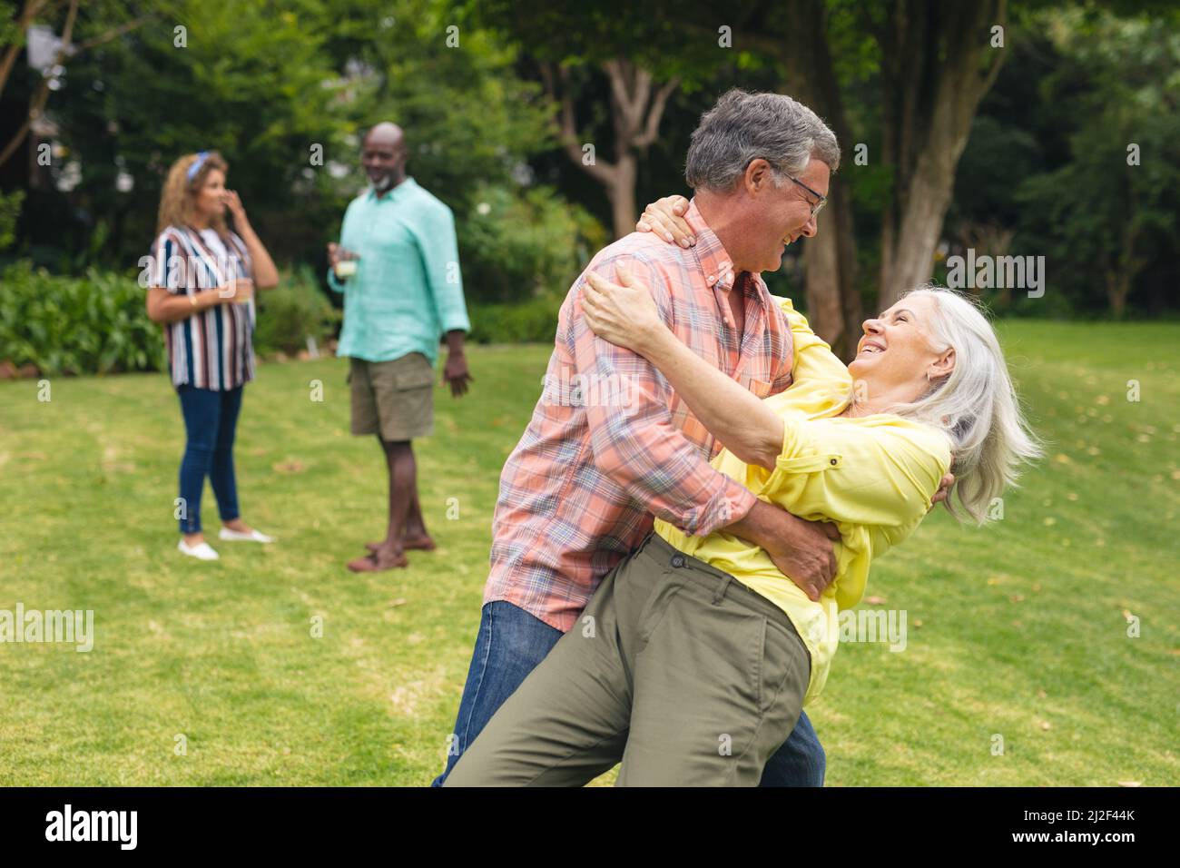 Happy caucasian senior couple dancing while friends in background ...