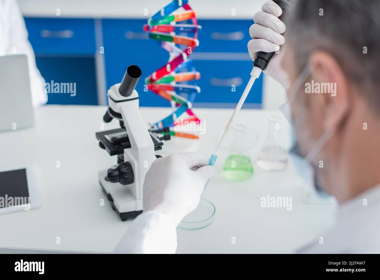 blurred geneticist in medical mask working with micropipette near ...