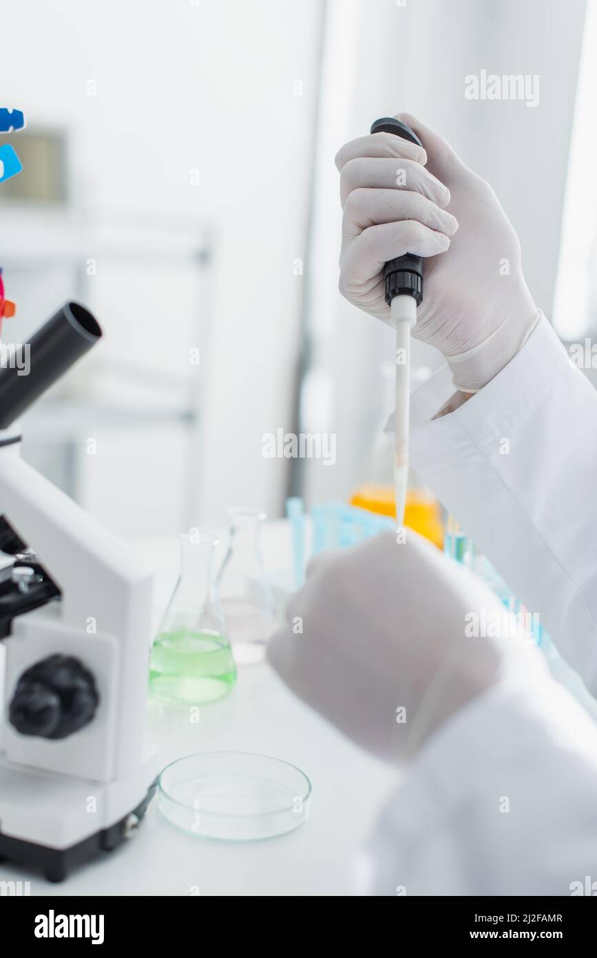 cropped view of bioengineer with micropipette working near blurred ...