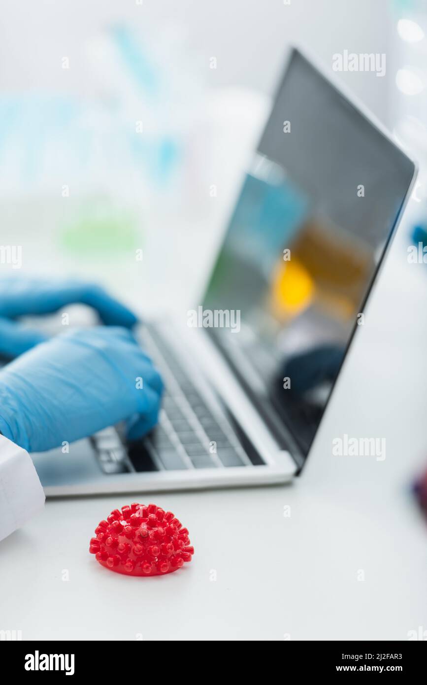 partial view of virologist typing on laptop with blank screen near red ...