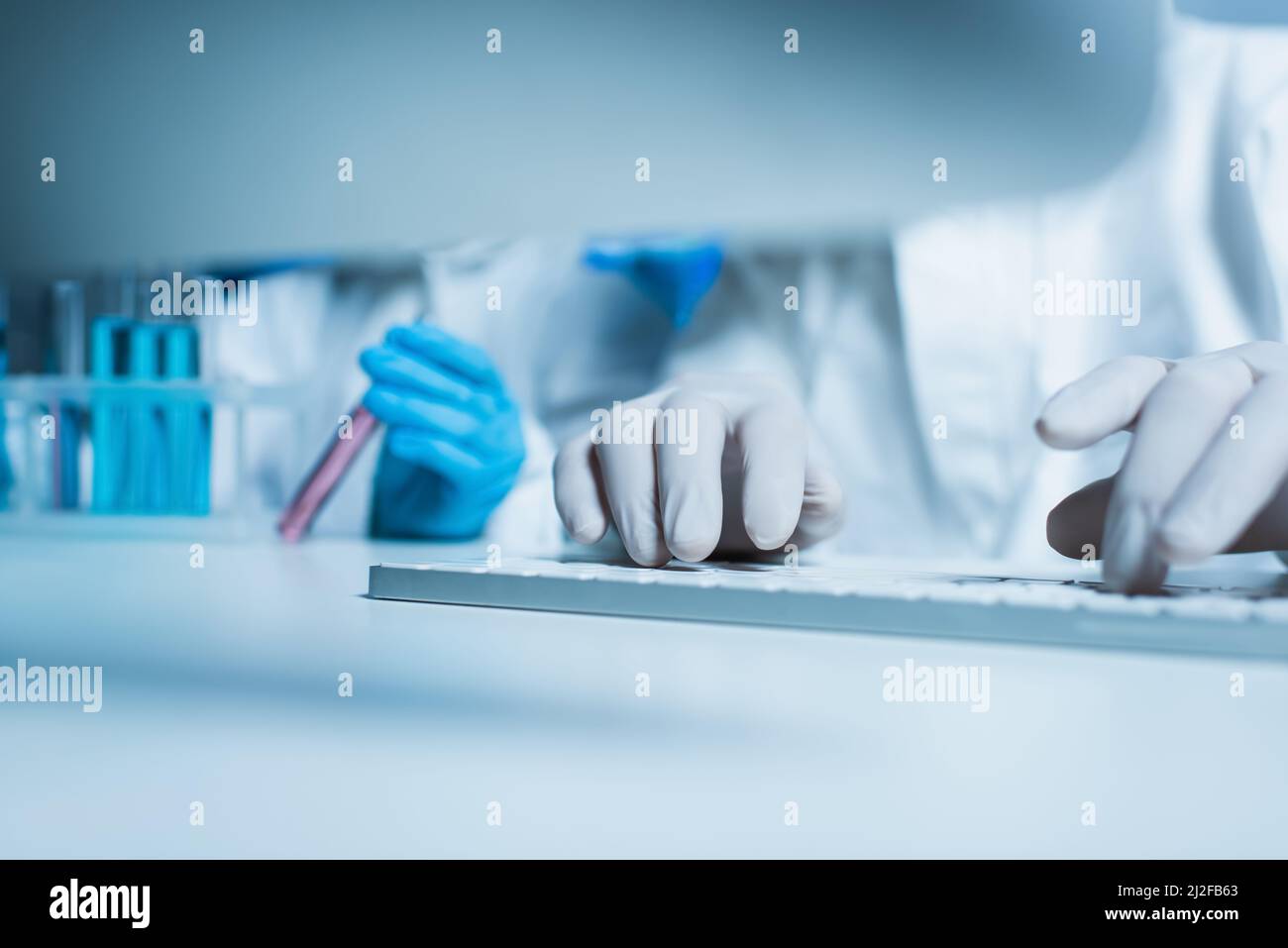 partial view of bioengineer in latex gloves typing on computer keyboard ...