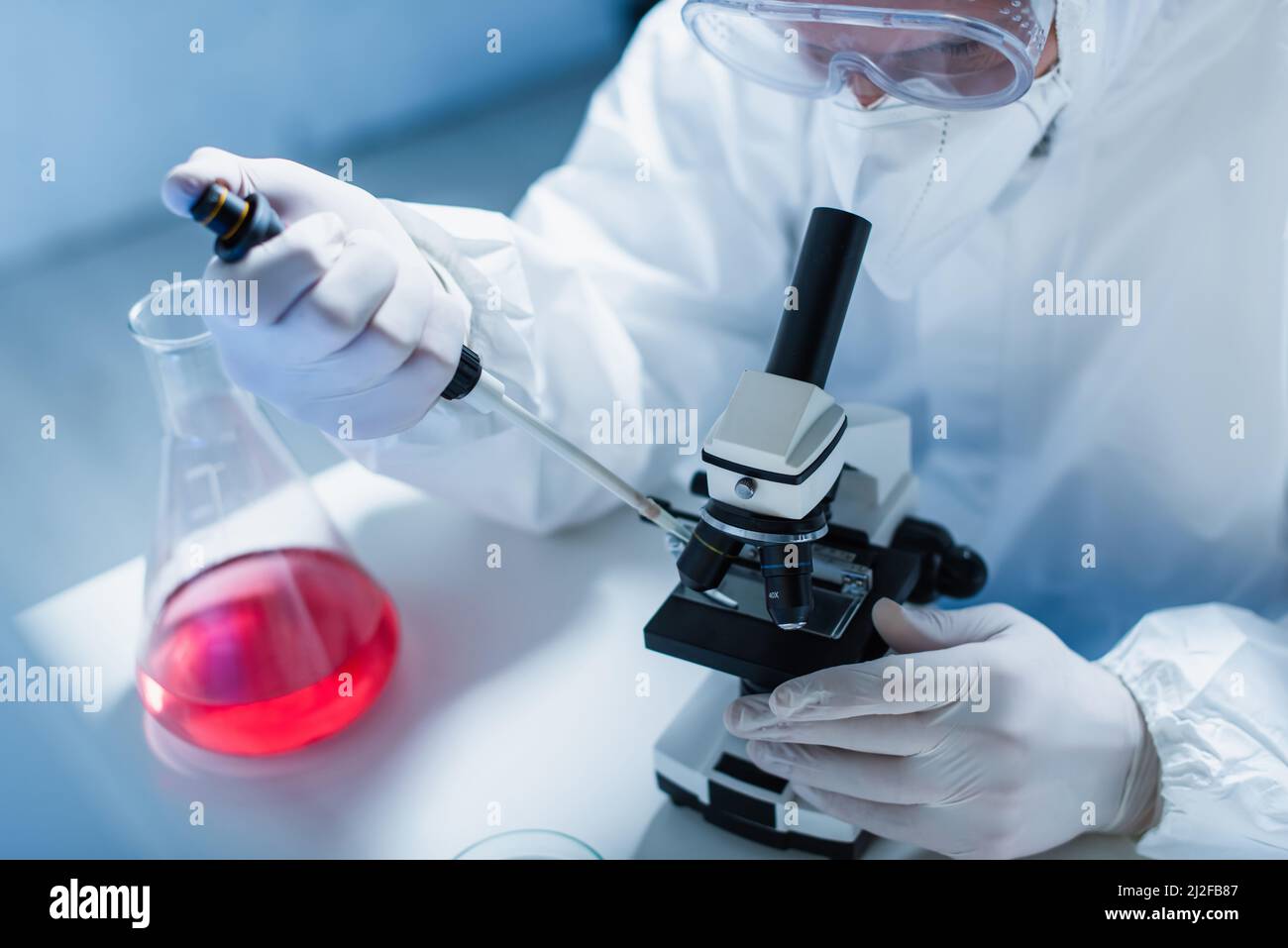 bioengineer in hazmat suit holding micropipette near microscope and ...