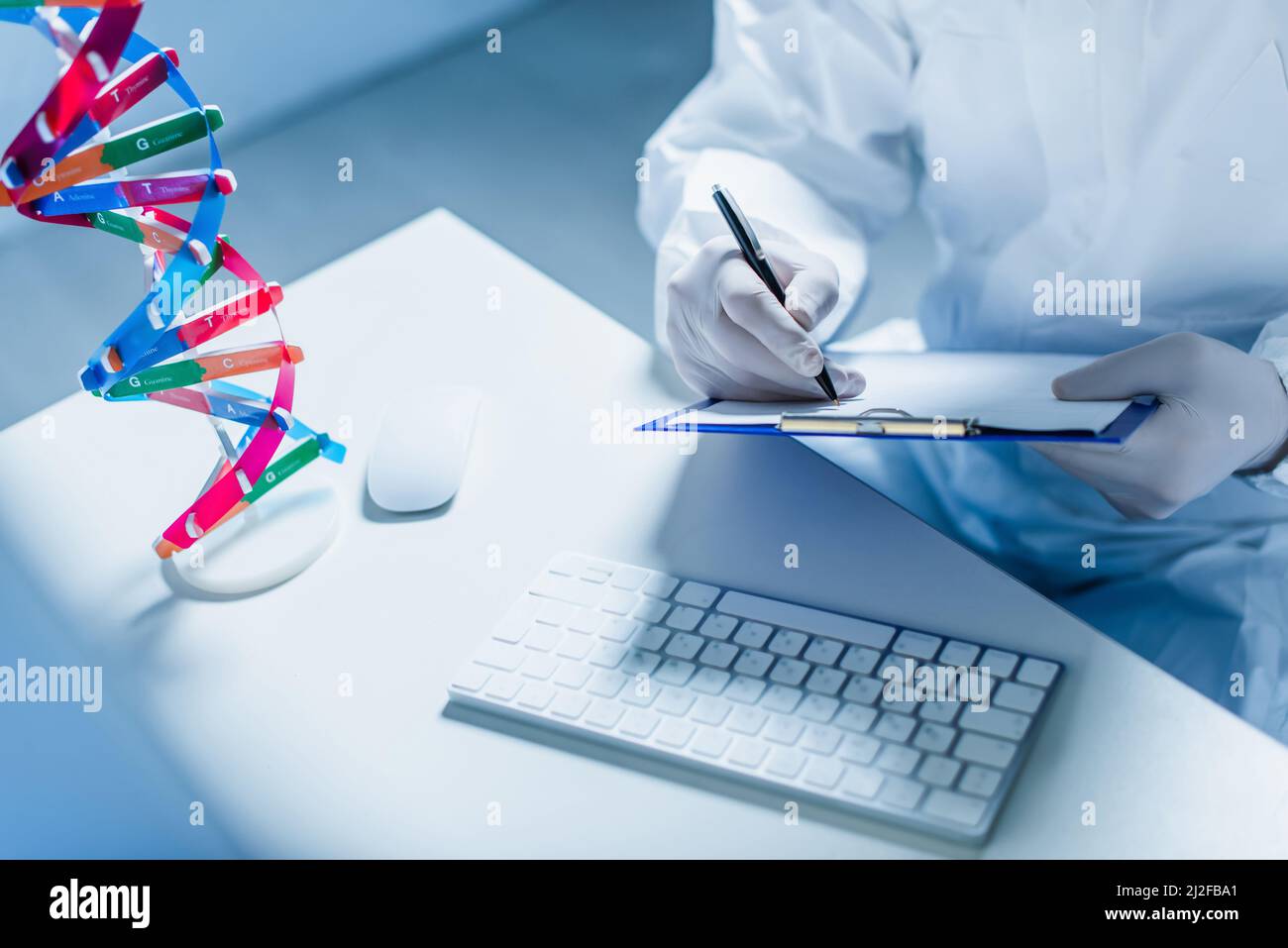 cropped view of scientist writing on clipboard near dna model and ...
