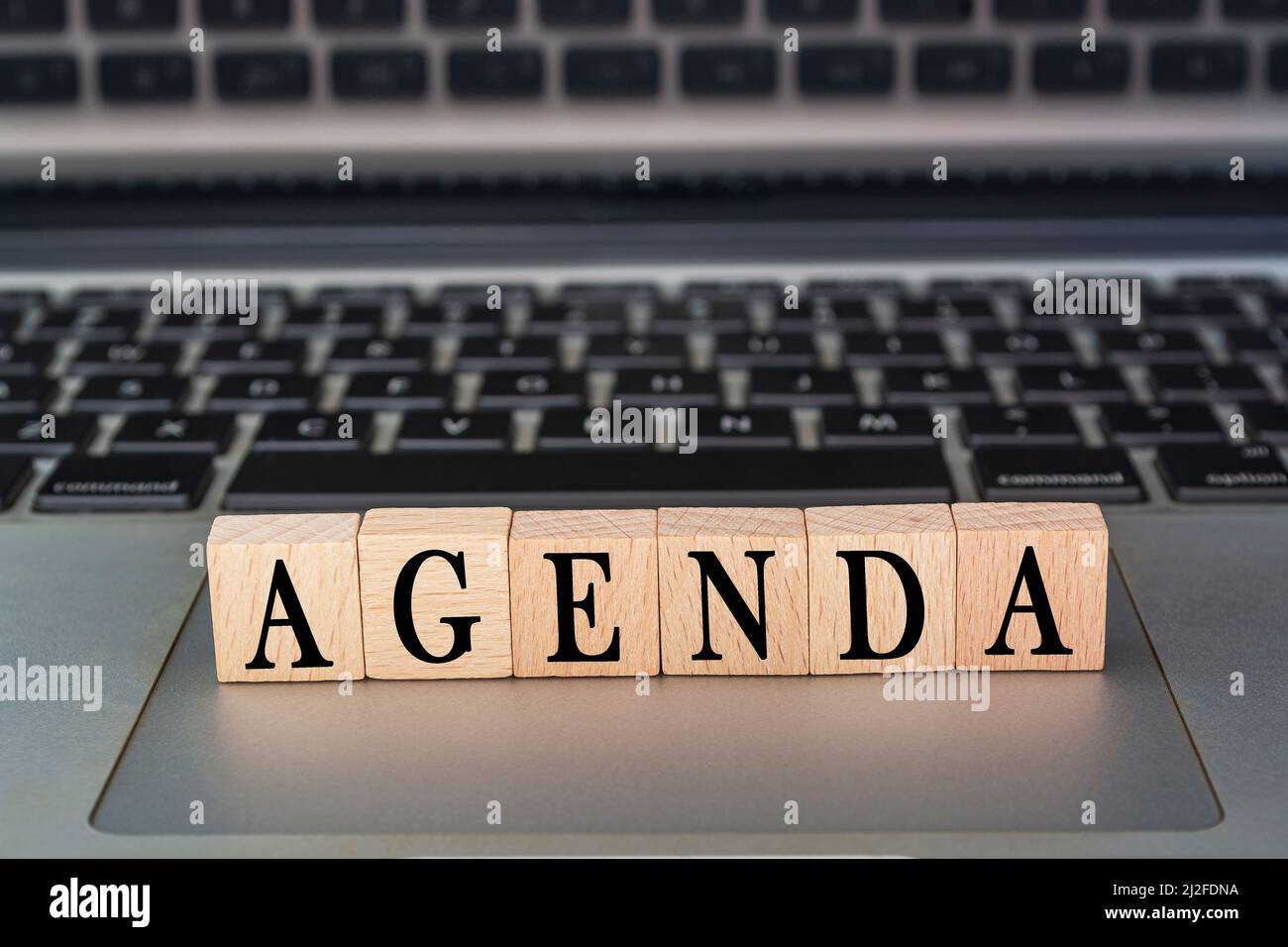 Agenda text on wooden block cube placed on laptop or notebook. Business ...