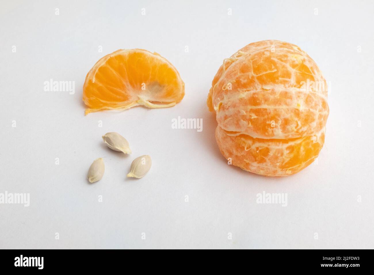 Still life with wedges tangerine and three seeds on white background ...