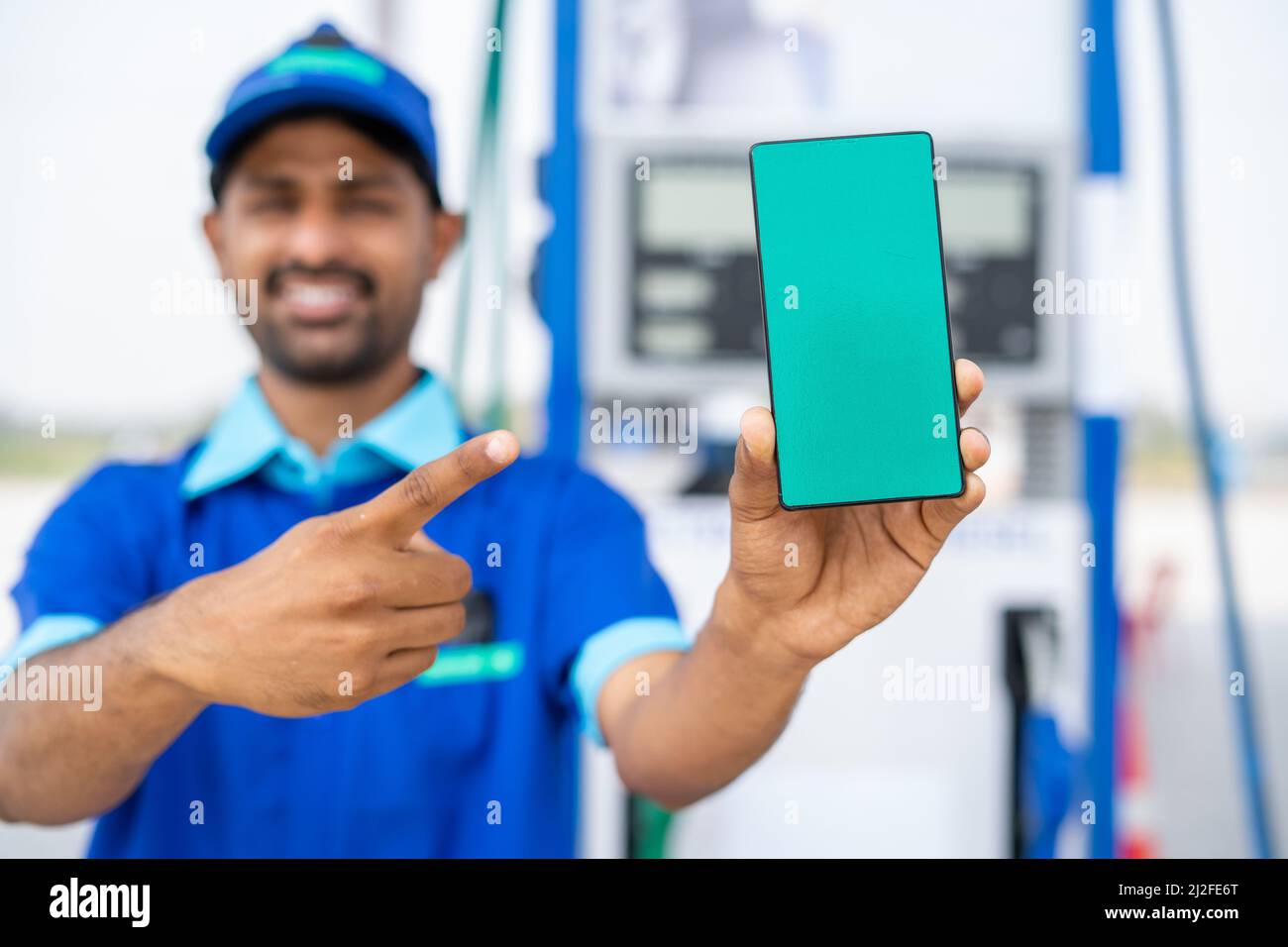 focus on phone, Smiling petrol pump worker showing green screen mobile ...