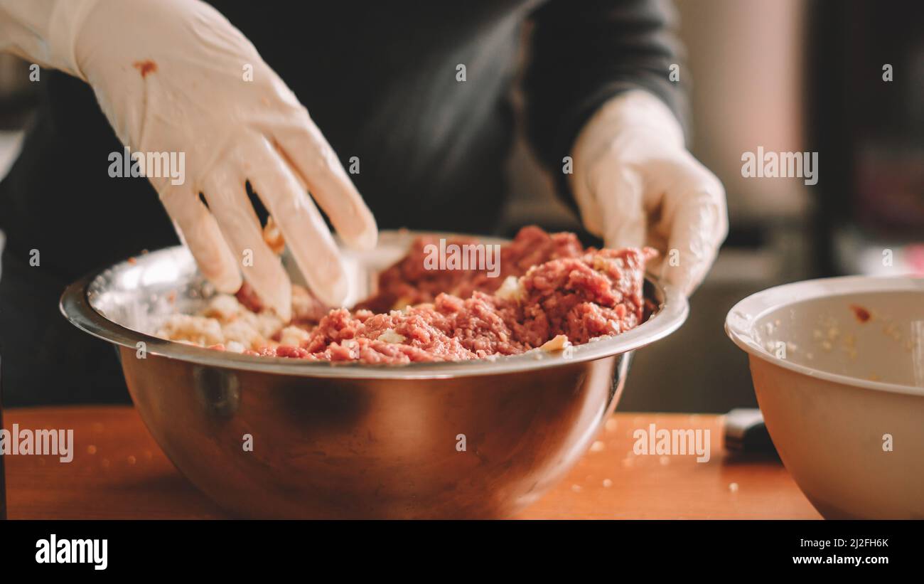 A closeup of a chef's hands mixing a raw meat mixture with rubber ...