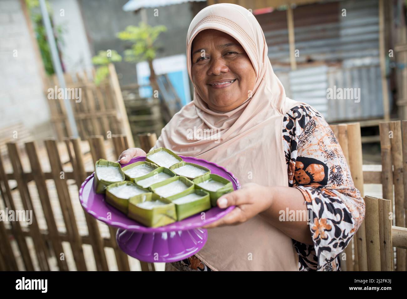 A woman displays freshly made sweet rice cakes wrapped in banana leaves ...