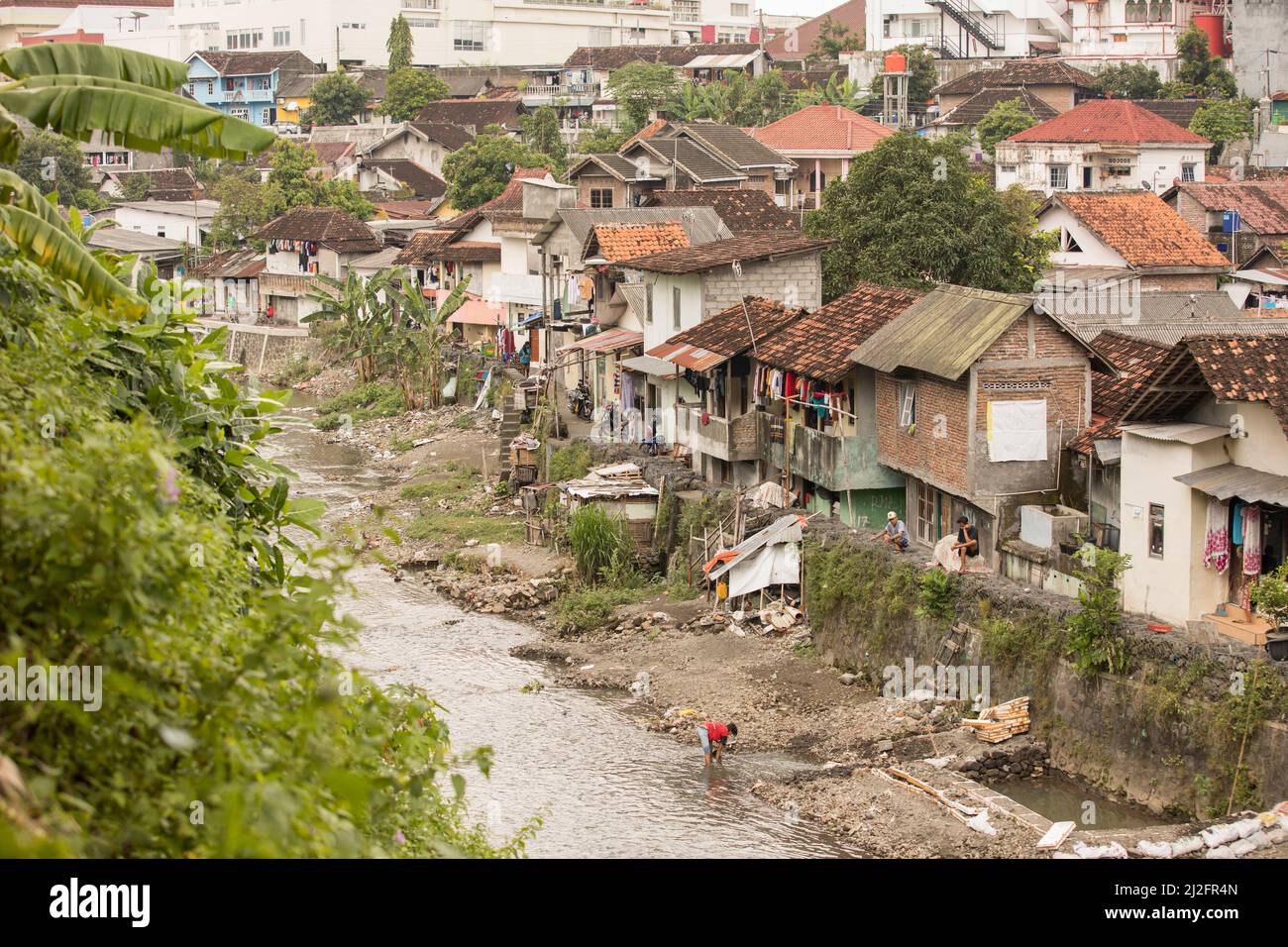Crowded colorful slum dwellings sit along side a sewage drainage canal ...