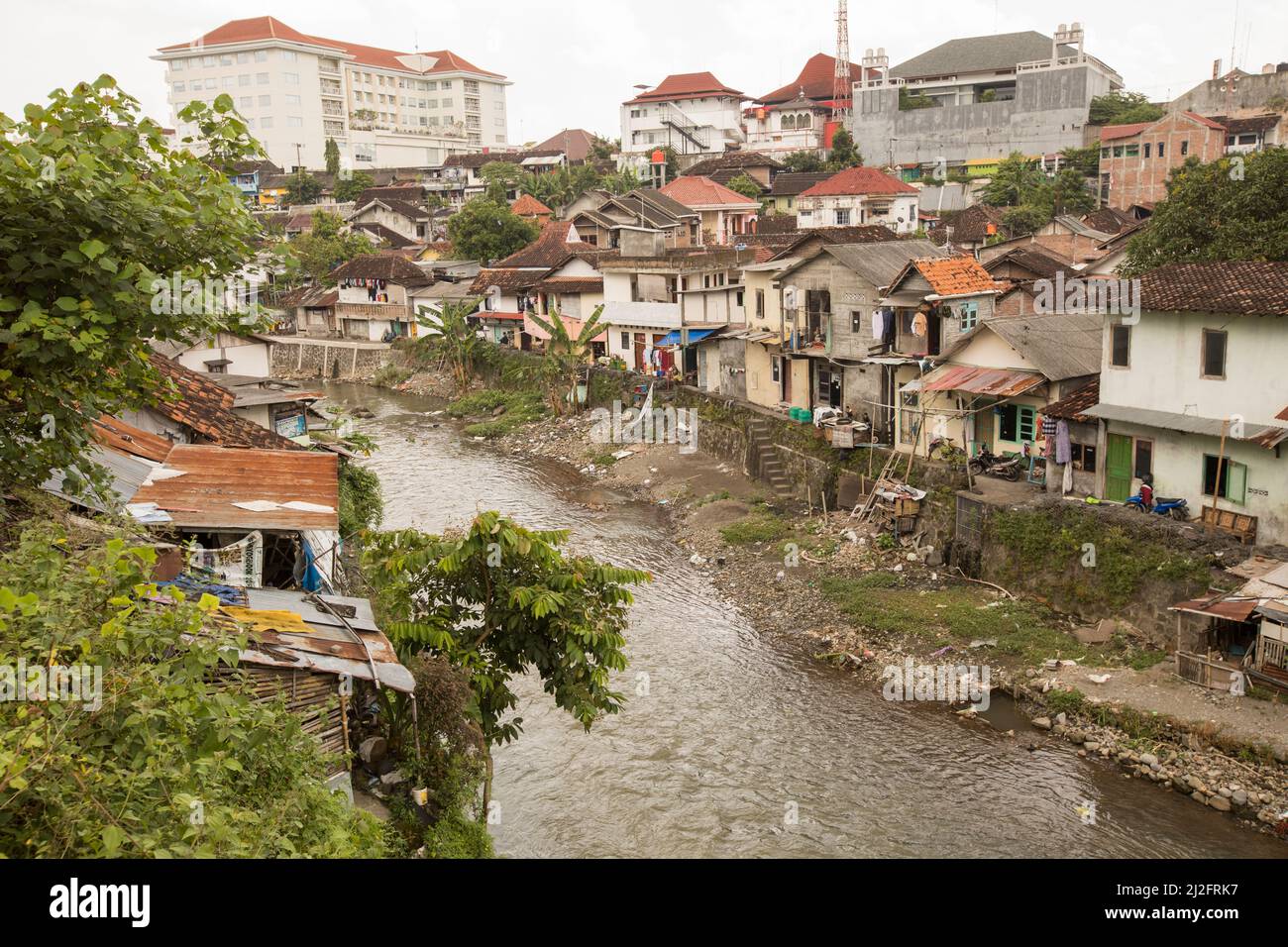 Crowded colorful slum dwellings sit along side a sewage drainage canal ...
