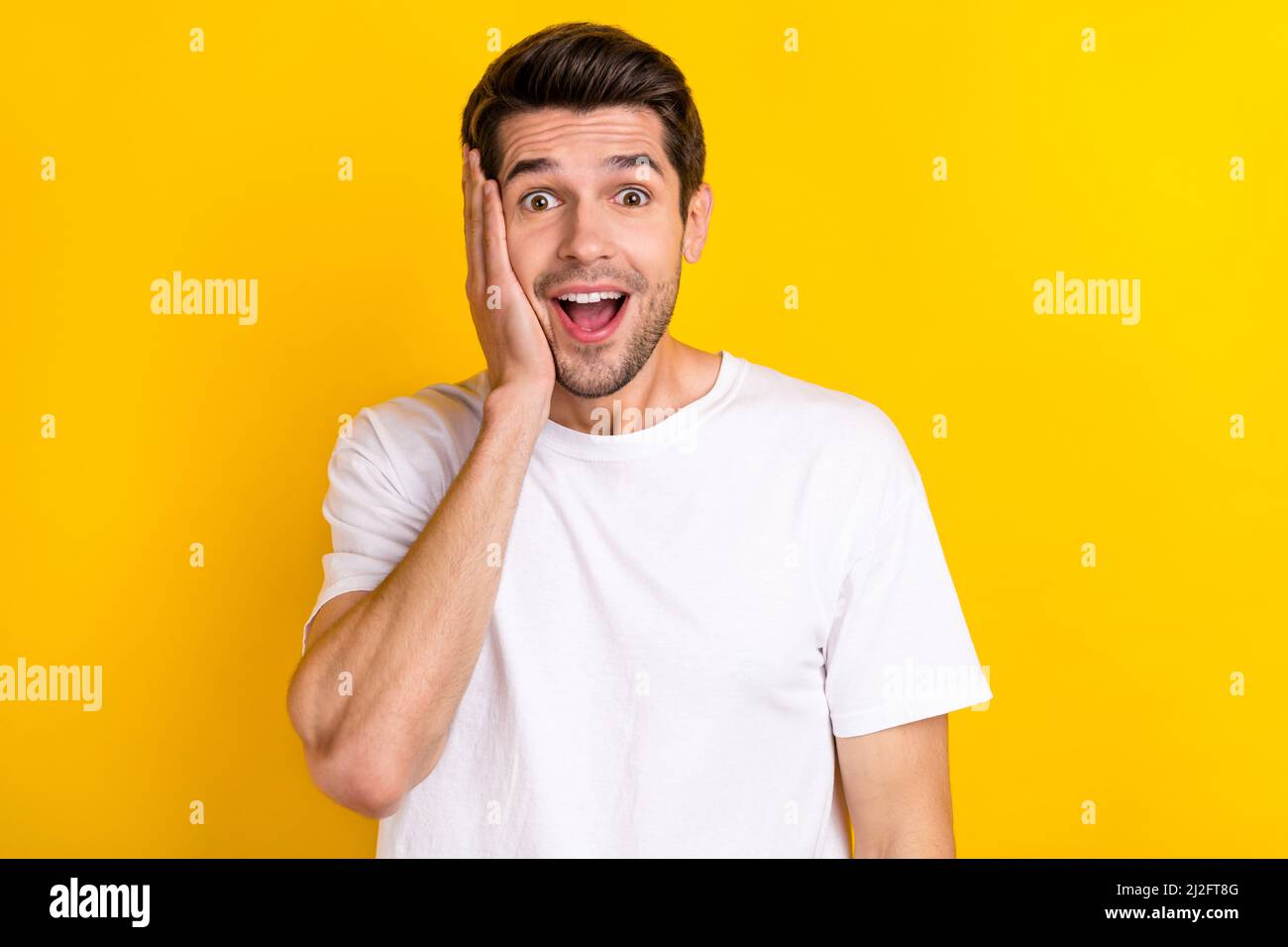Photo of impressed millennial brunet guy palms face wear white t-shirt ...