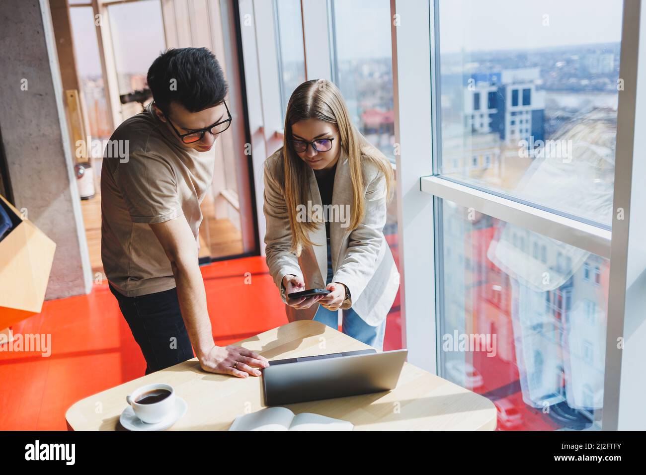 Two colleagues, a man and a woman manager, stand near a table with a ...
