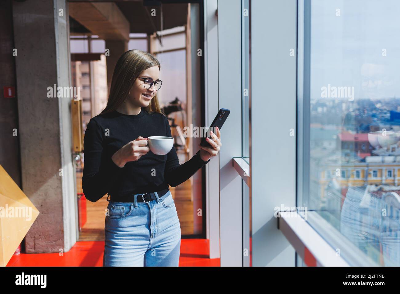 European woman drinks coffee and looks out the window in a cafe. A ...