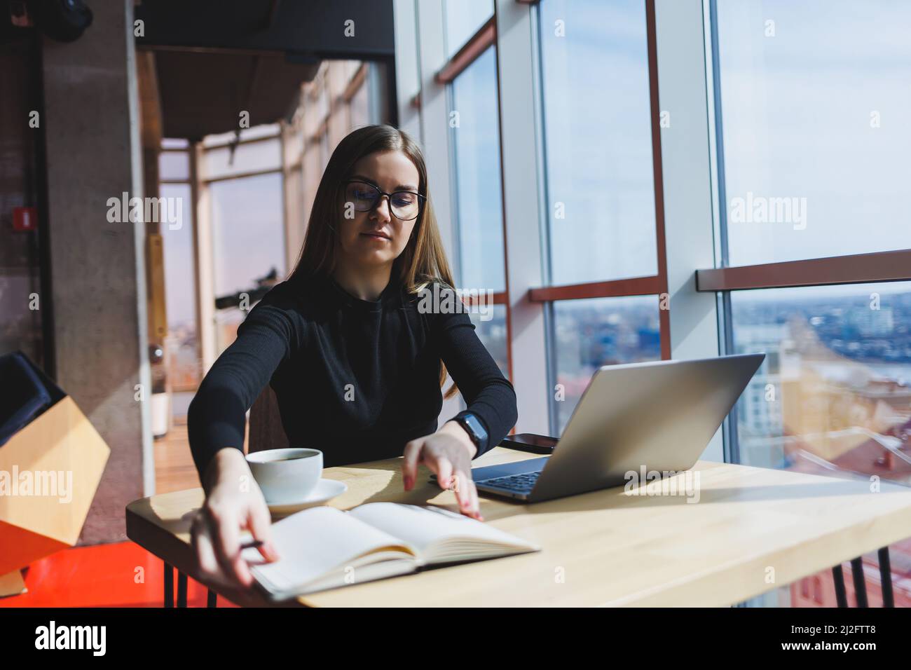 Online work in a cafe. Happy girl in casual clothes and glasses using a ...