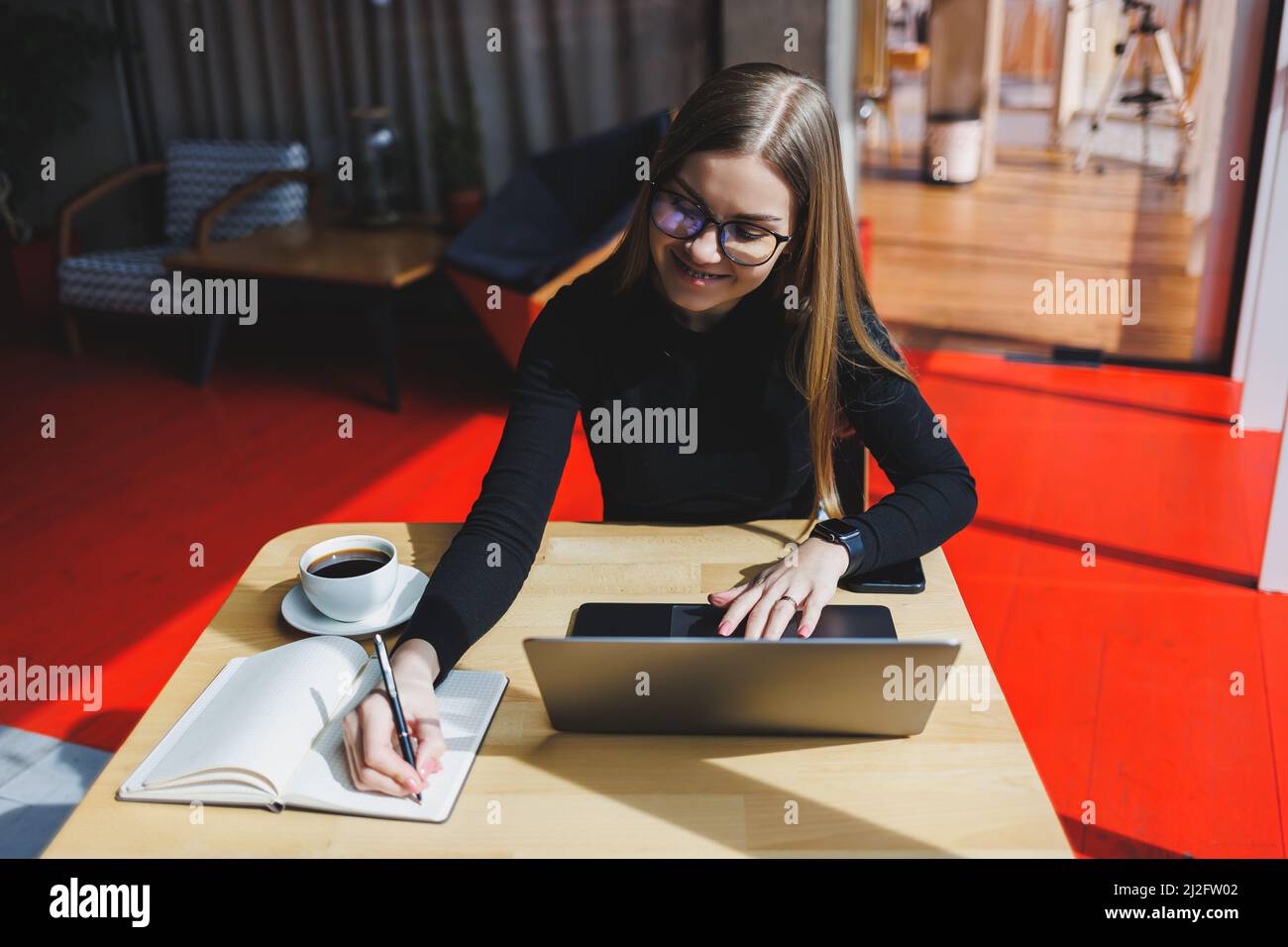 Online work in a cafe. Happy girl in casual clothes and glasses using a ...
