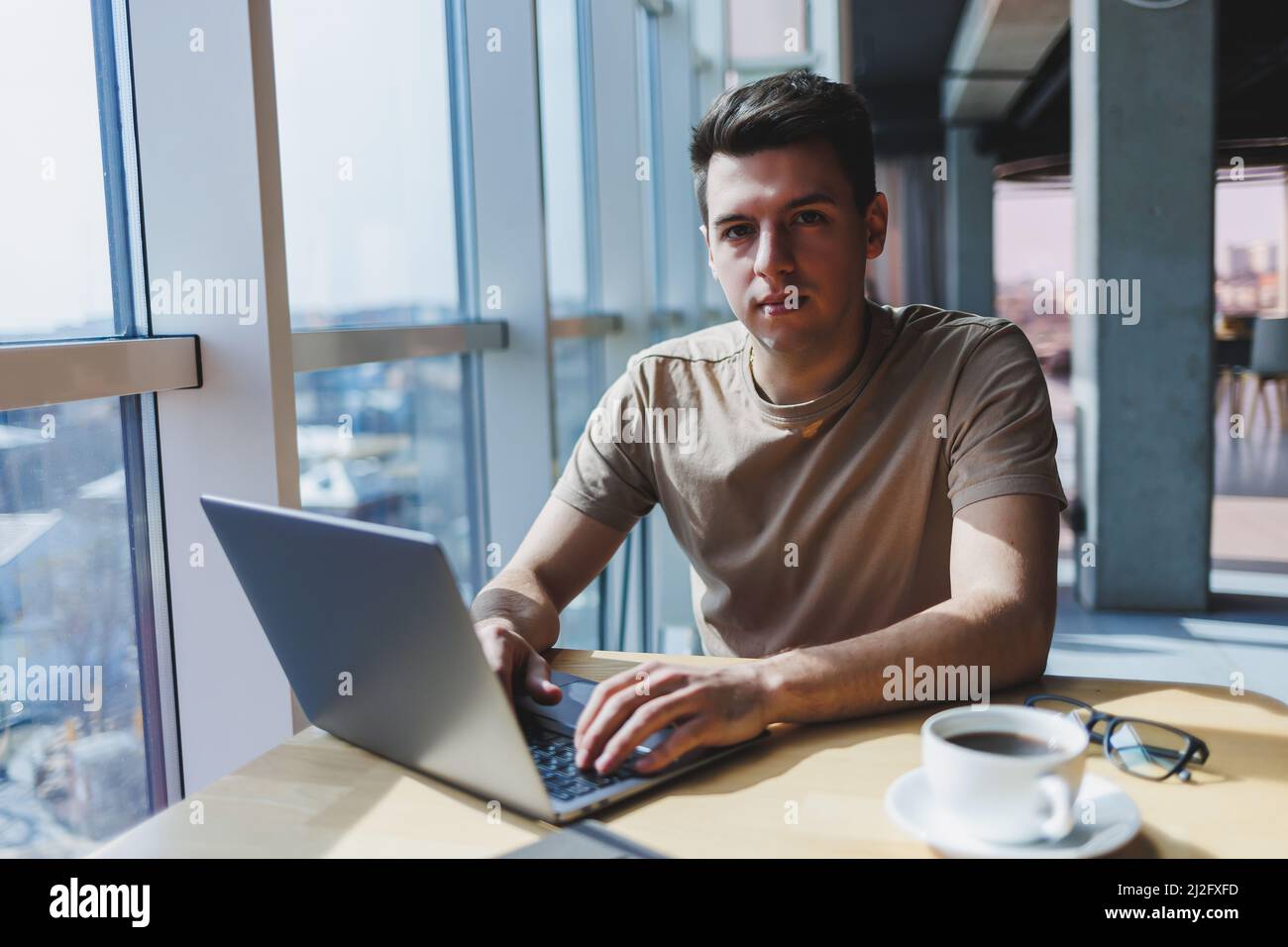 A young attractive male freelancer sits in the interior of a coffee ...