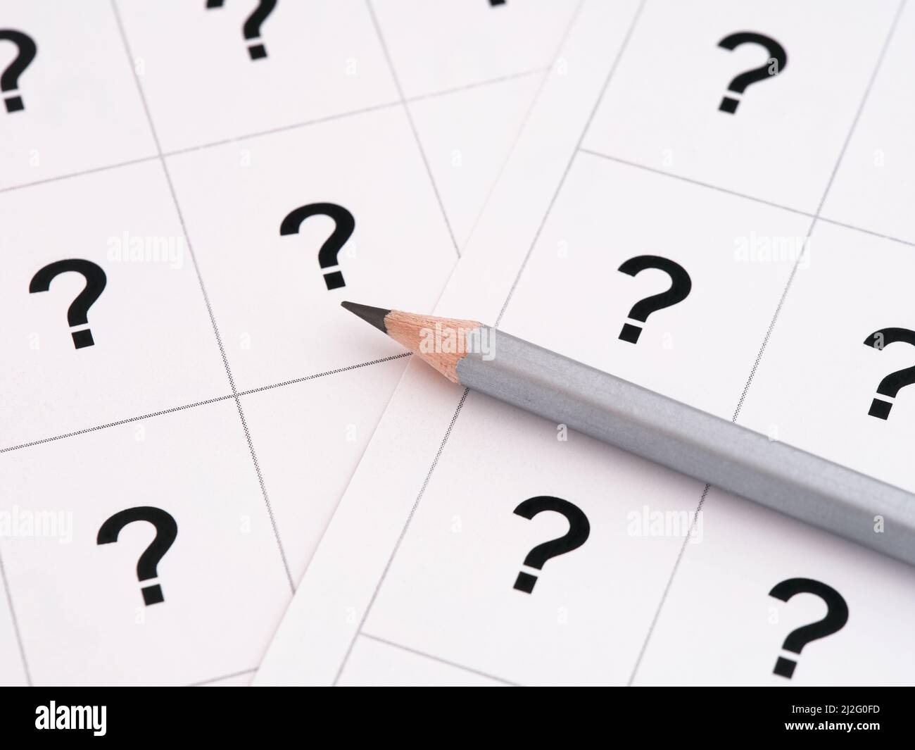 A gray pencil laying on pieces of paper that have question marks on ...