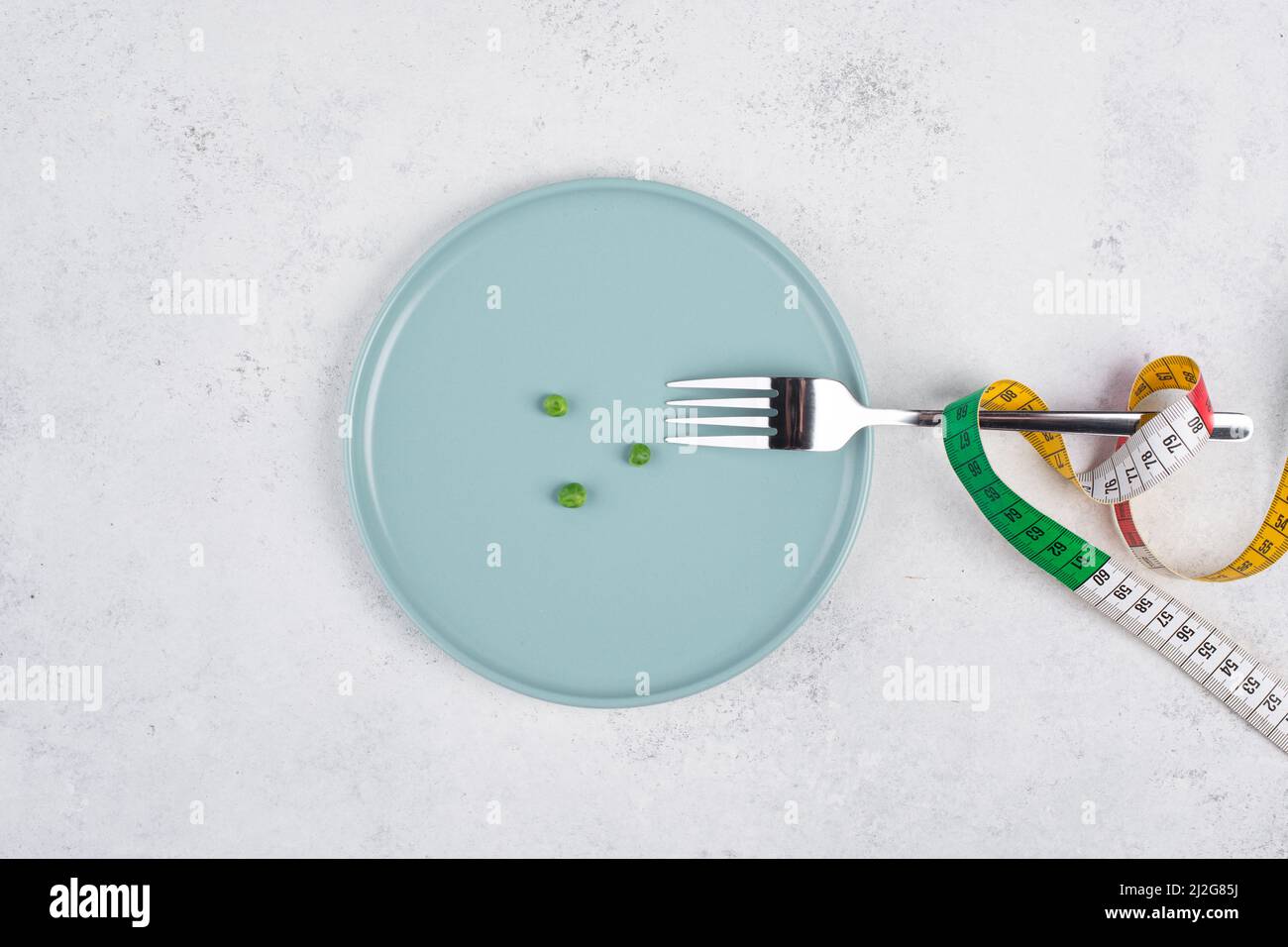 One single pea on a plate, hand with tape measure and fork, diet and ...