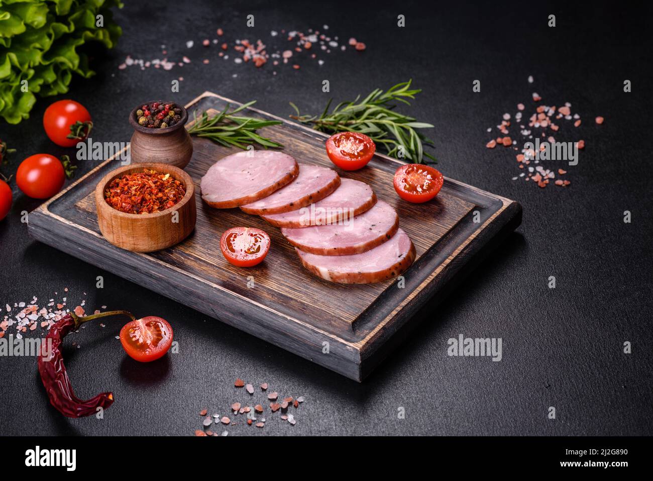 Delicious fresh ham cut with slices on a wooden cutting board on a dark ...
