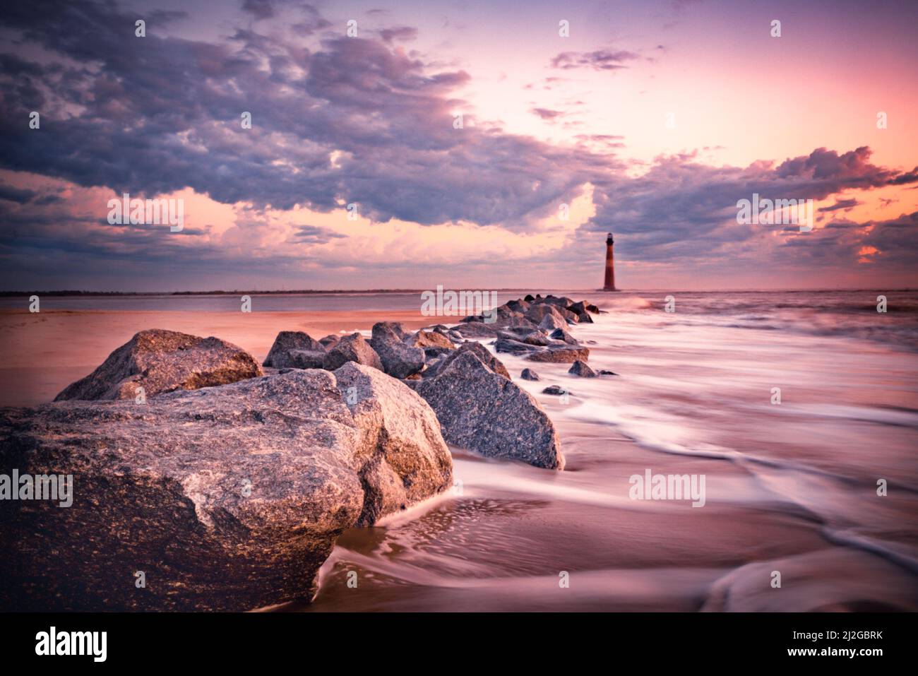 Seascape with rock jetty, ocean and lighthouse in the distance Stock ...