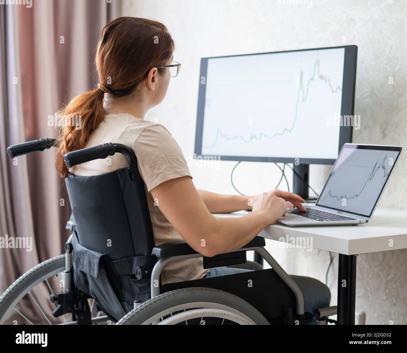 Caucasian woman in a wheelchair typing with a laptop from home. Remote ...