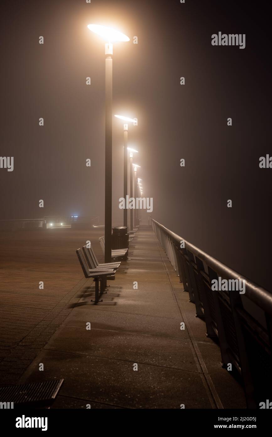 A vertical shot of the city street covered with fog with benches under ...