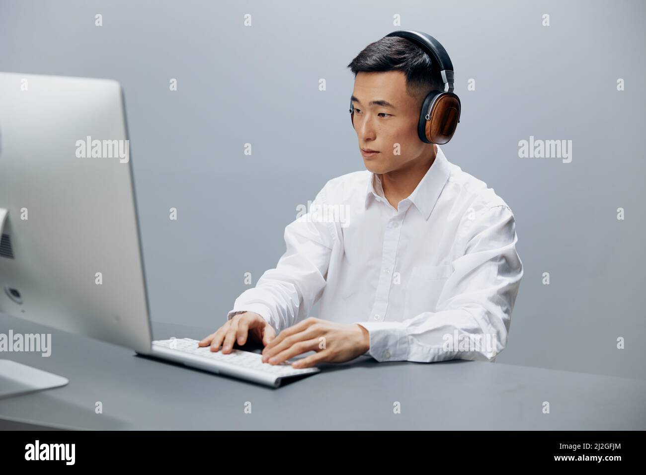 Asian man in headphones at the table in front of the computer ...