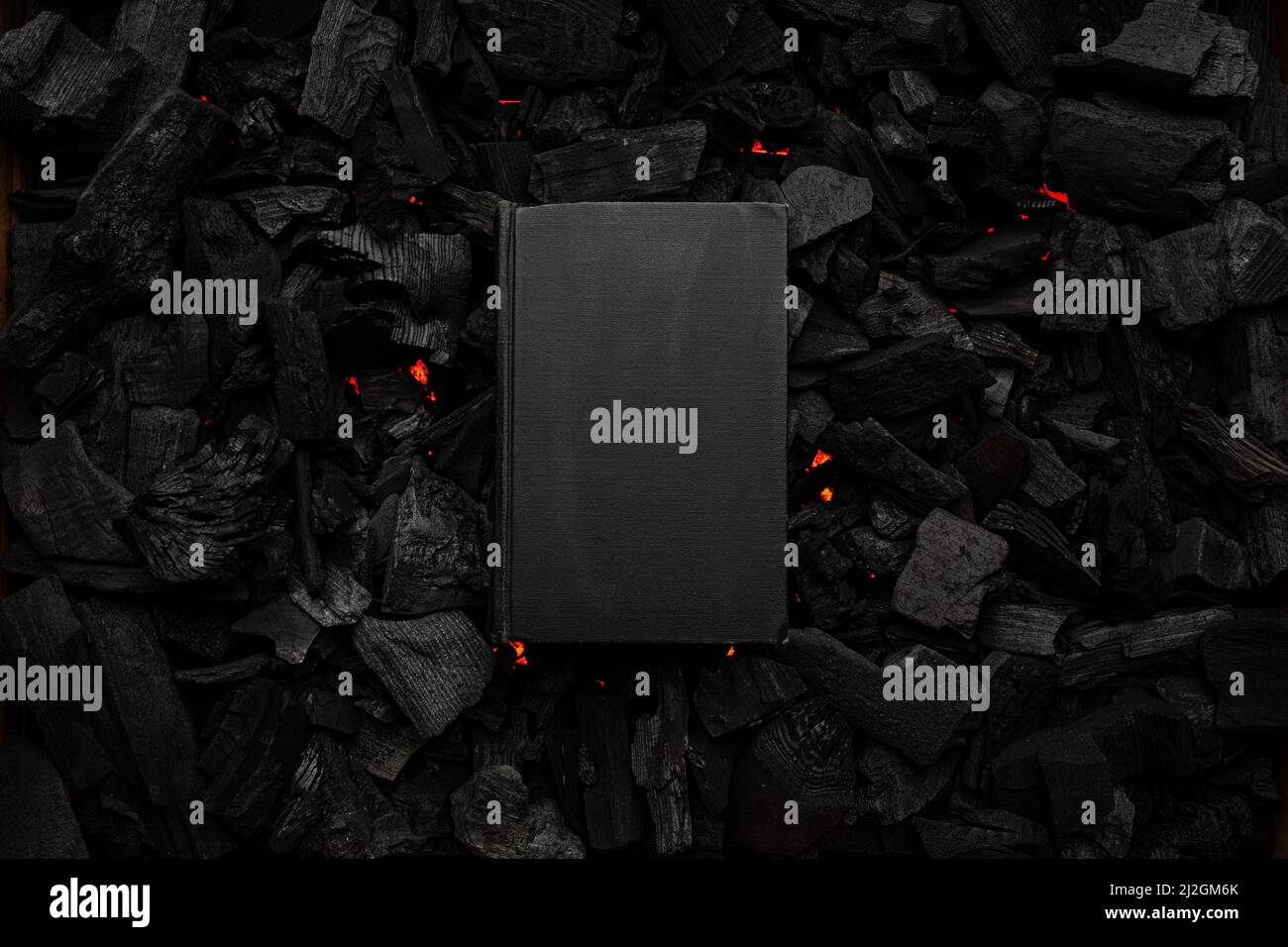A closed book with a black cover on smoldering charcoal. Textured dark ...