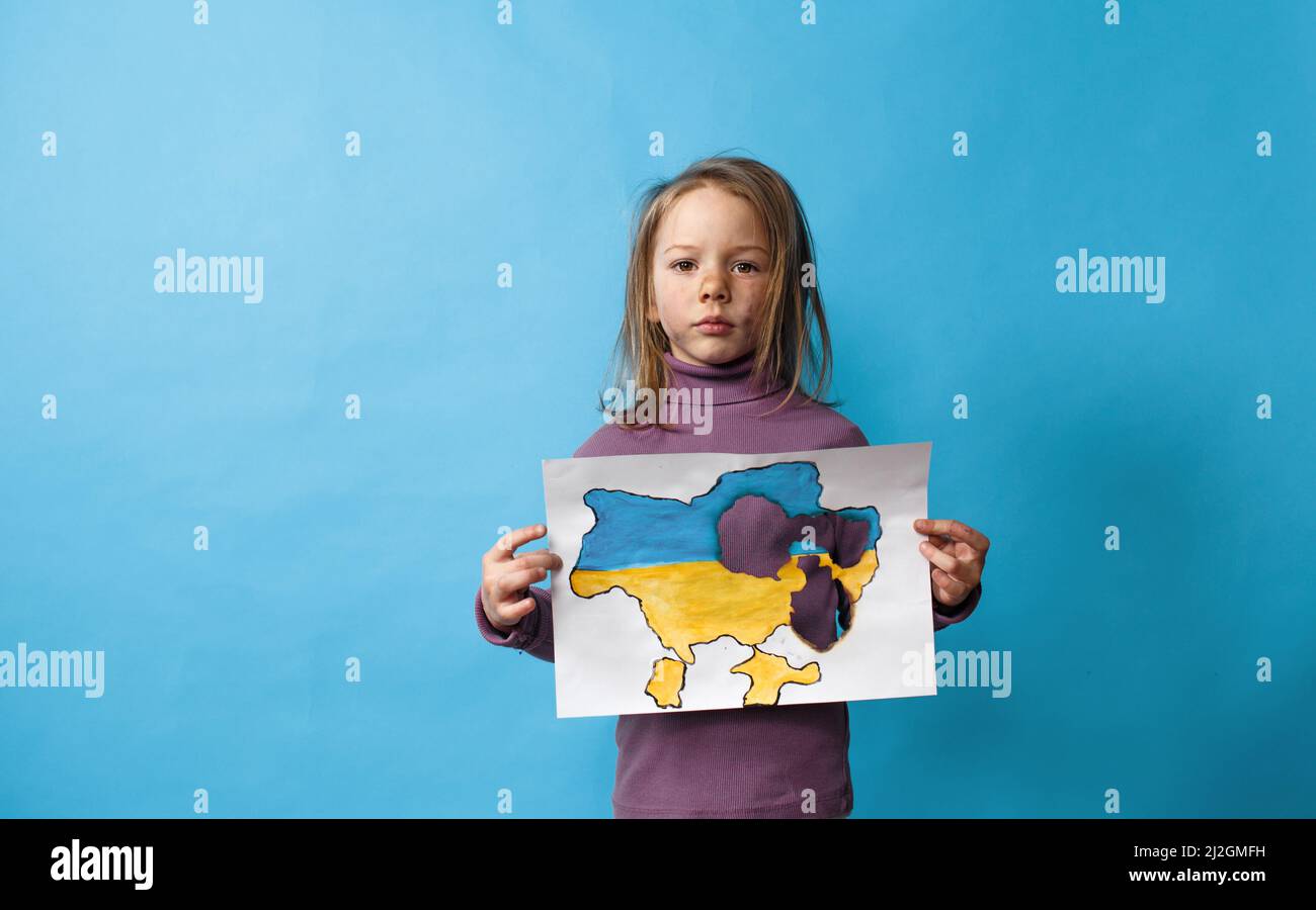 a little girl on a blue background holds a burnt map of Ukraine in her ...