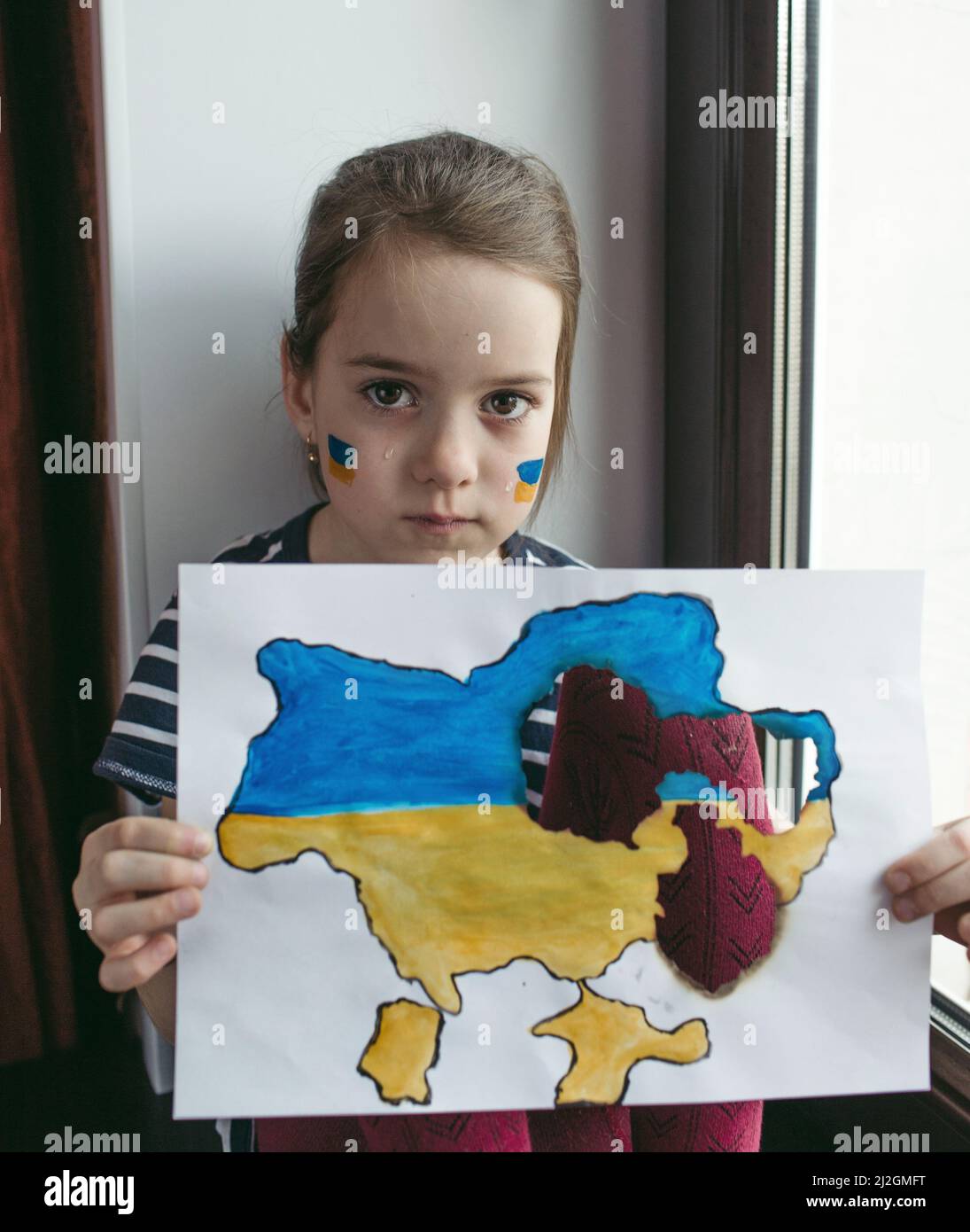 a little Ukrainian girl with tears in her eyes is sitting at the window ...