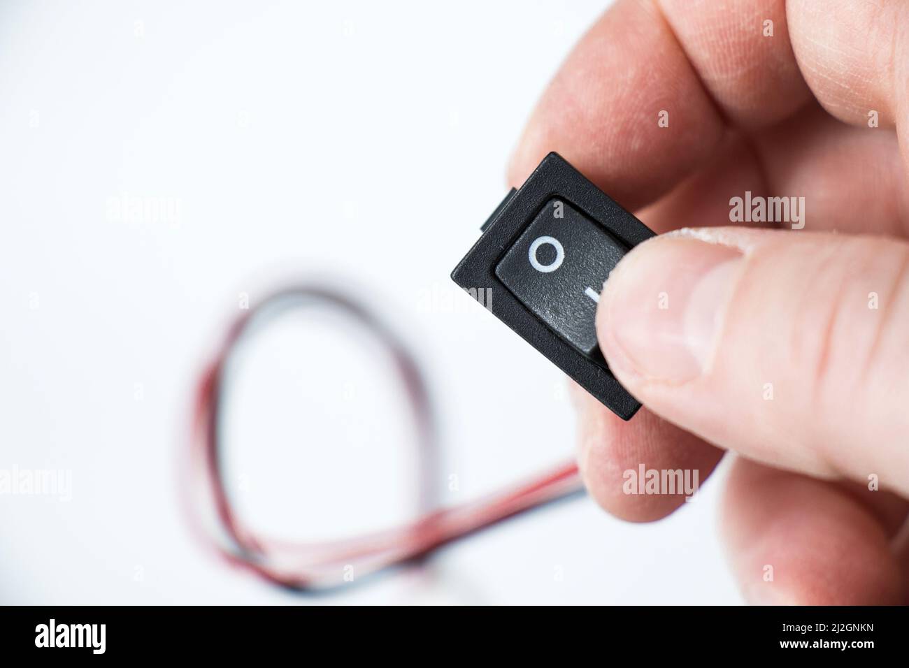 A person's hand holding the on and off button with red and black wires ...