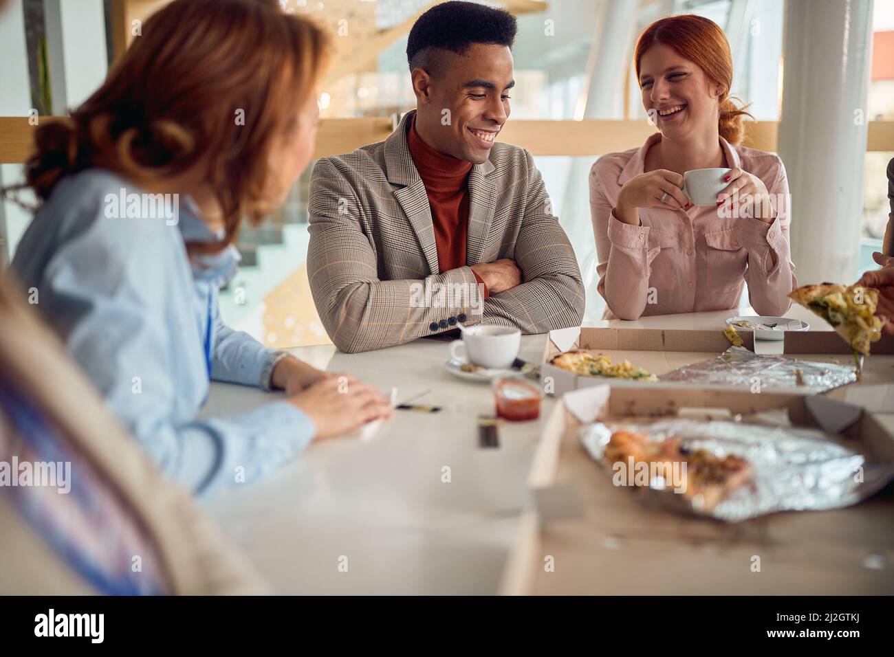 A group of young colleagues is enjoying lunch break at work in a ...