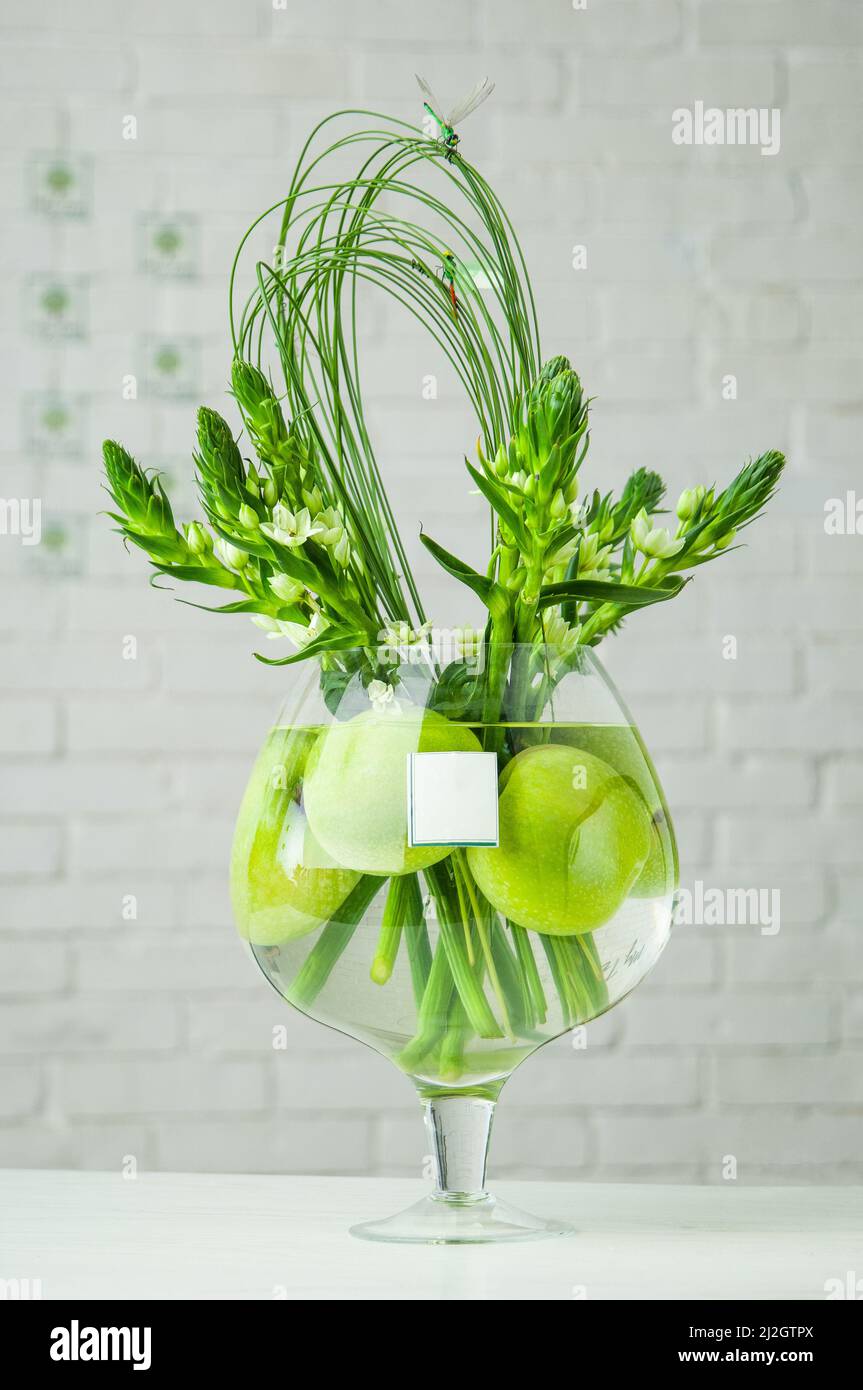 A vertical shot of Ornithogalum plant and apples in a large glass cup ...