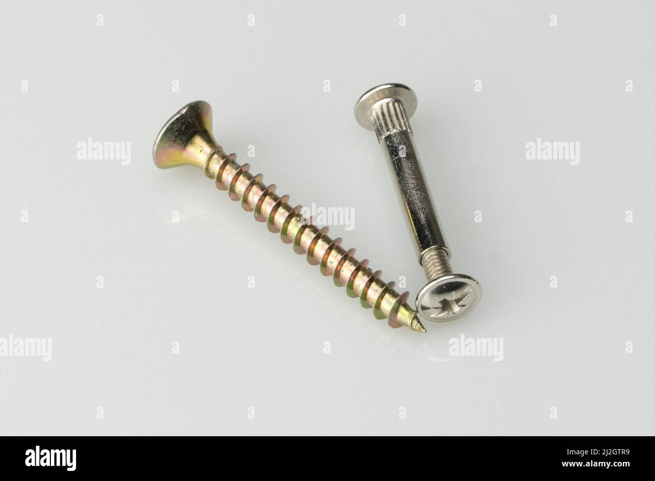 A closeup of a self-tapping screw and a coupling bolt on a white ...