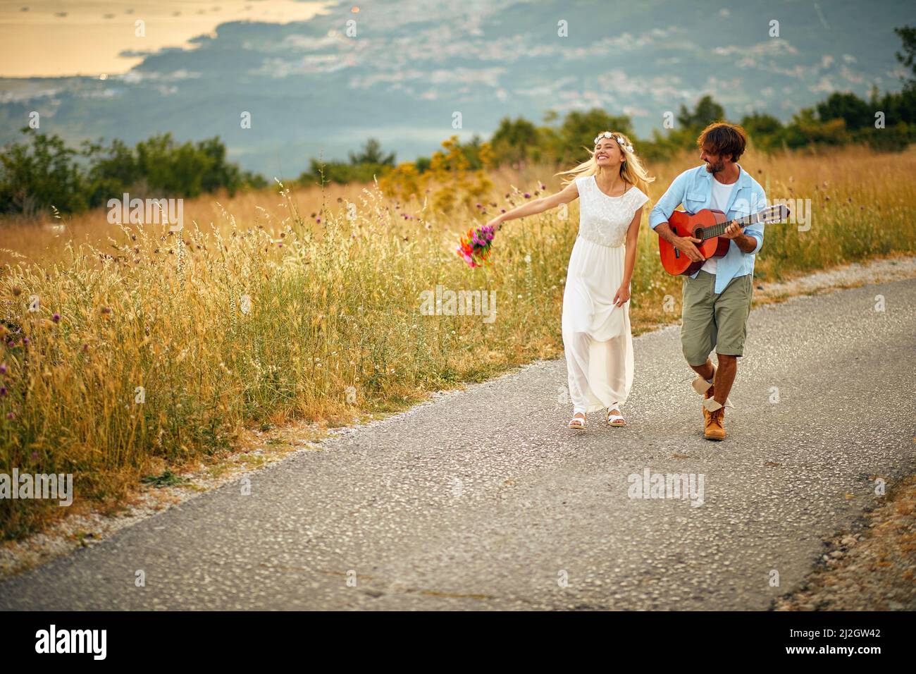 A young groom is playing guitar for his bride while they walking the ...