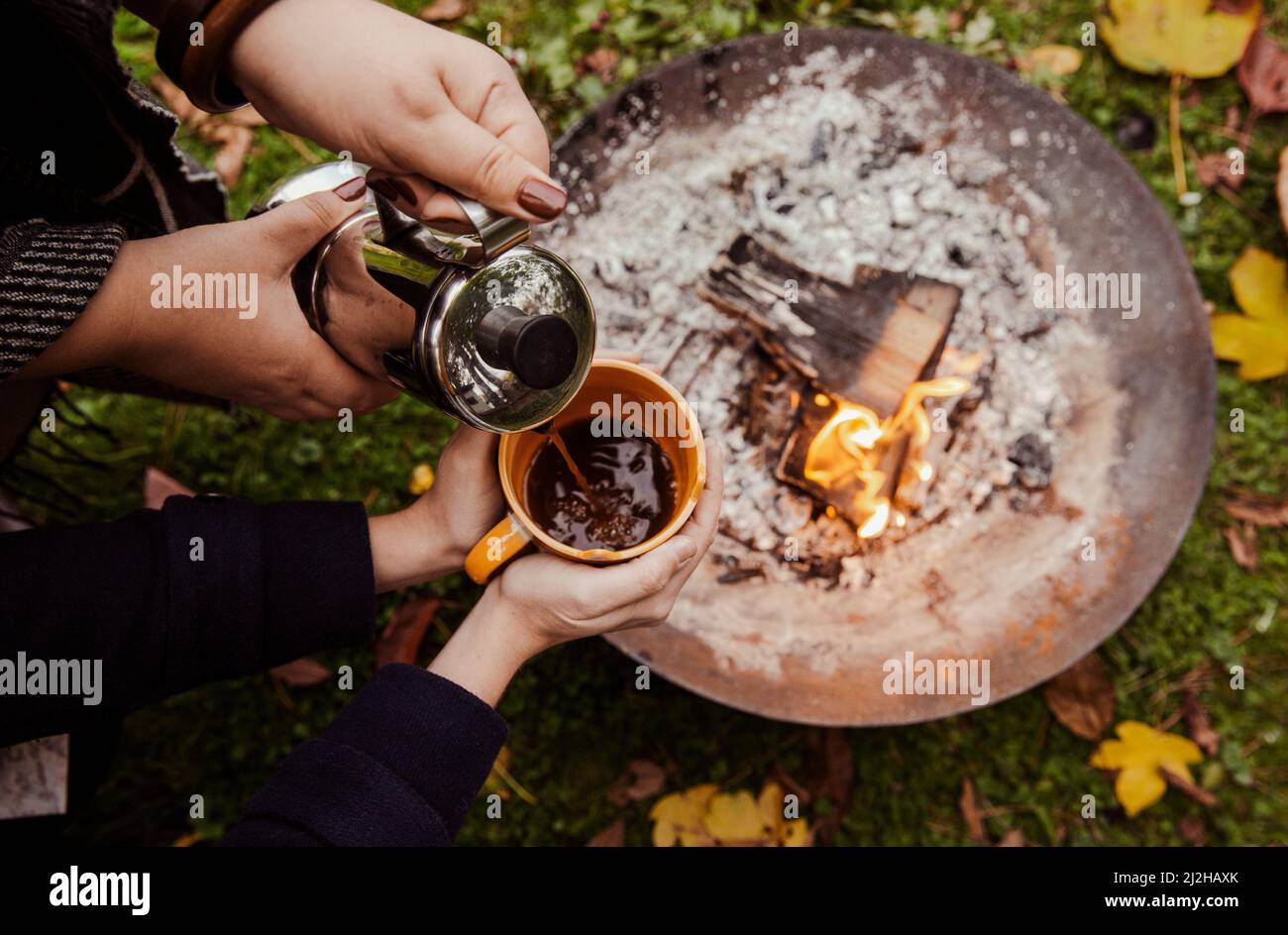 Overhead view of coffee being poured into mug above fire pit at picnic ...