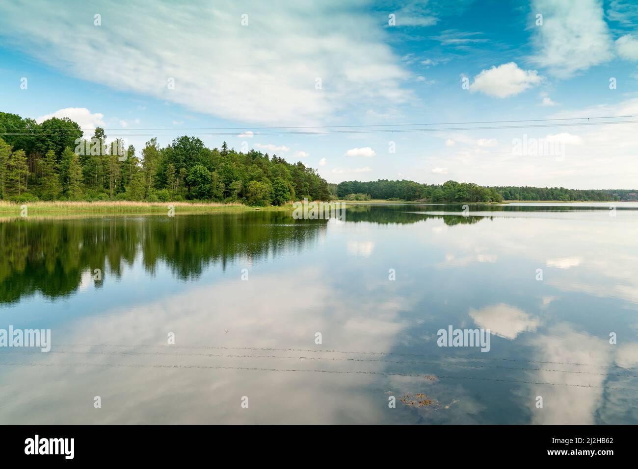 Sweden, Loftahammar, Calm sea surface reflecting trees and clouds Stock ...