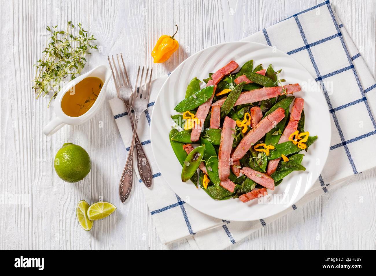 sugar snap peas with tuna slices, pepper, thyme on a white plate, on a wooden table with forks ...
