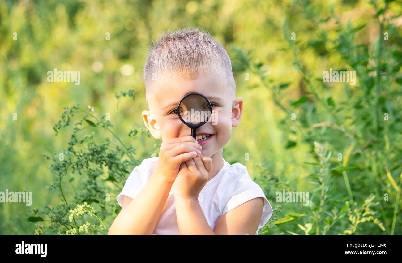 Young boy exploring nature in the meadow with a magnifying glass ...