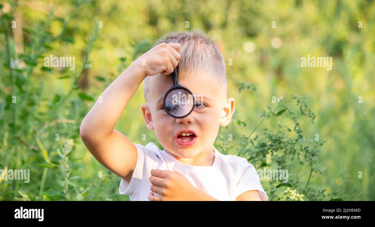 Young boy exploring nature in the meadow with a magnifying glass ...