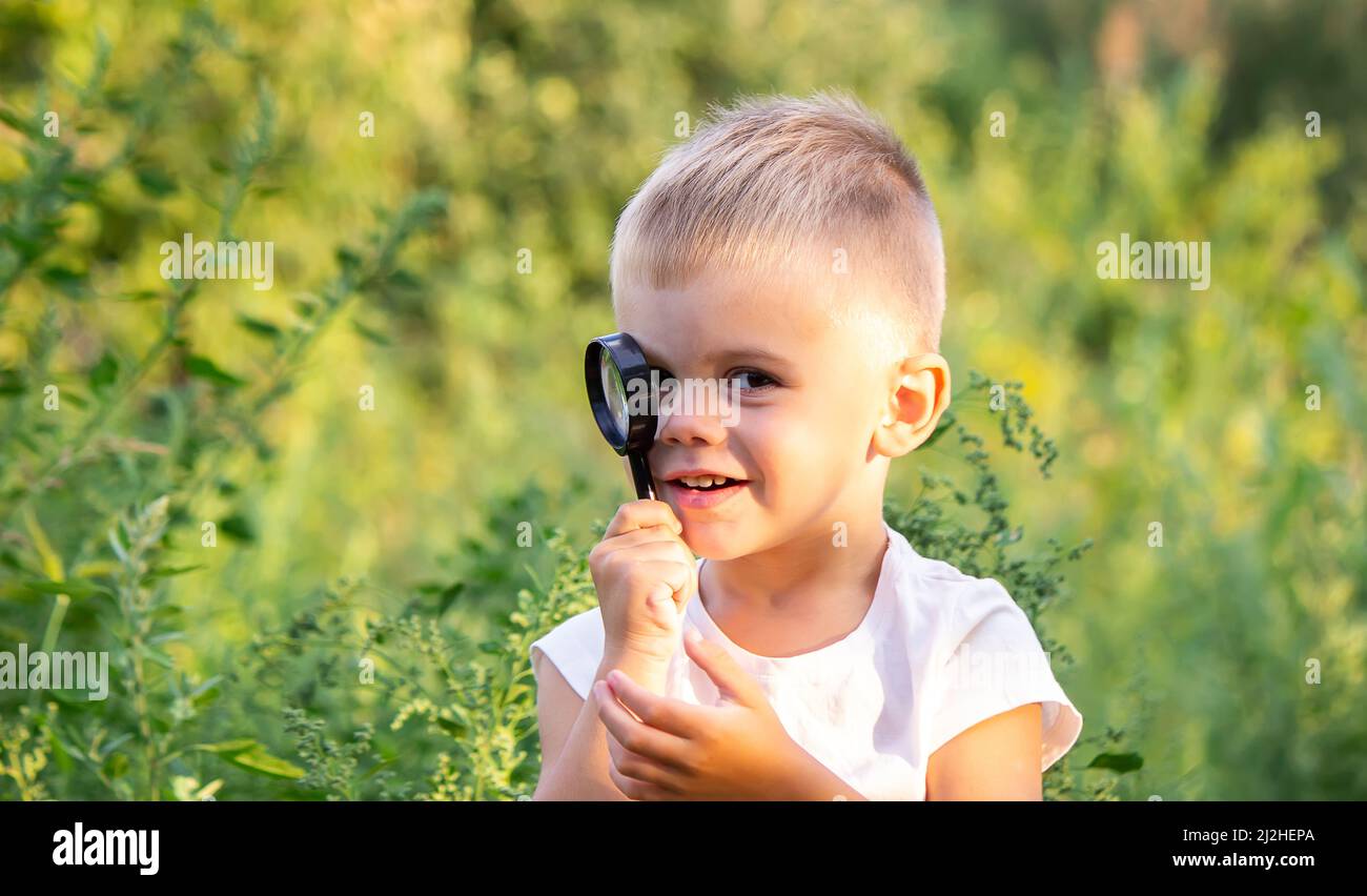 Young boy exploring nature in the meadow with a magnifying glass ...