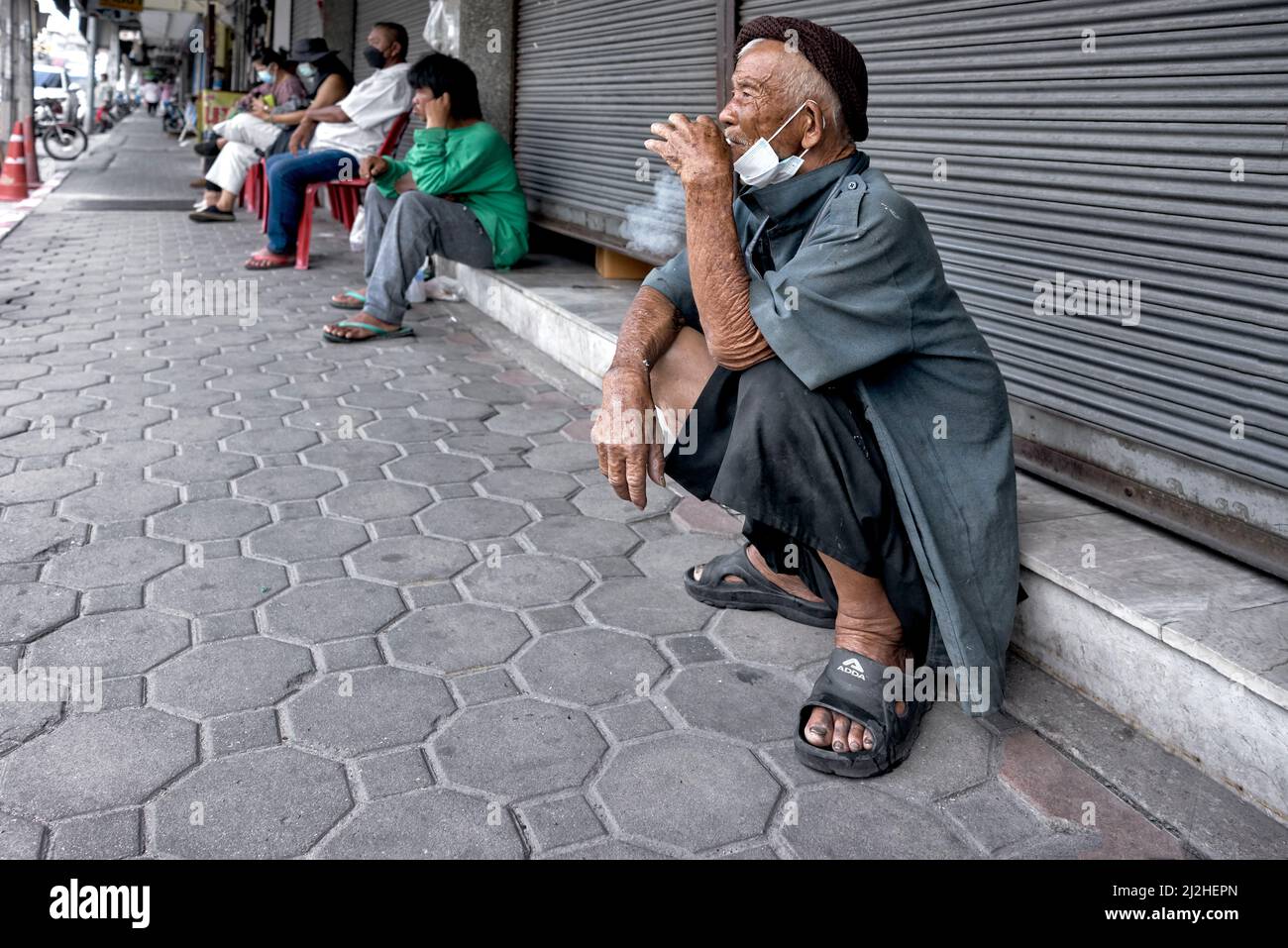 Thailand Elderly,, man ,squatting on the pavement whilst smoking a ...