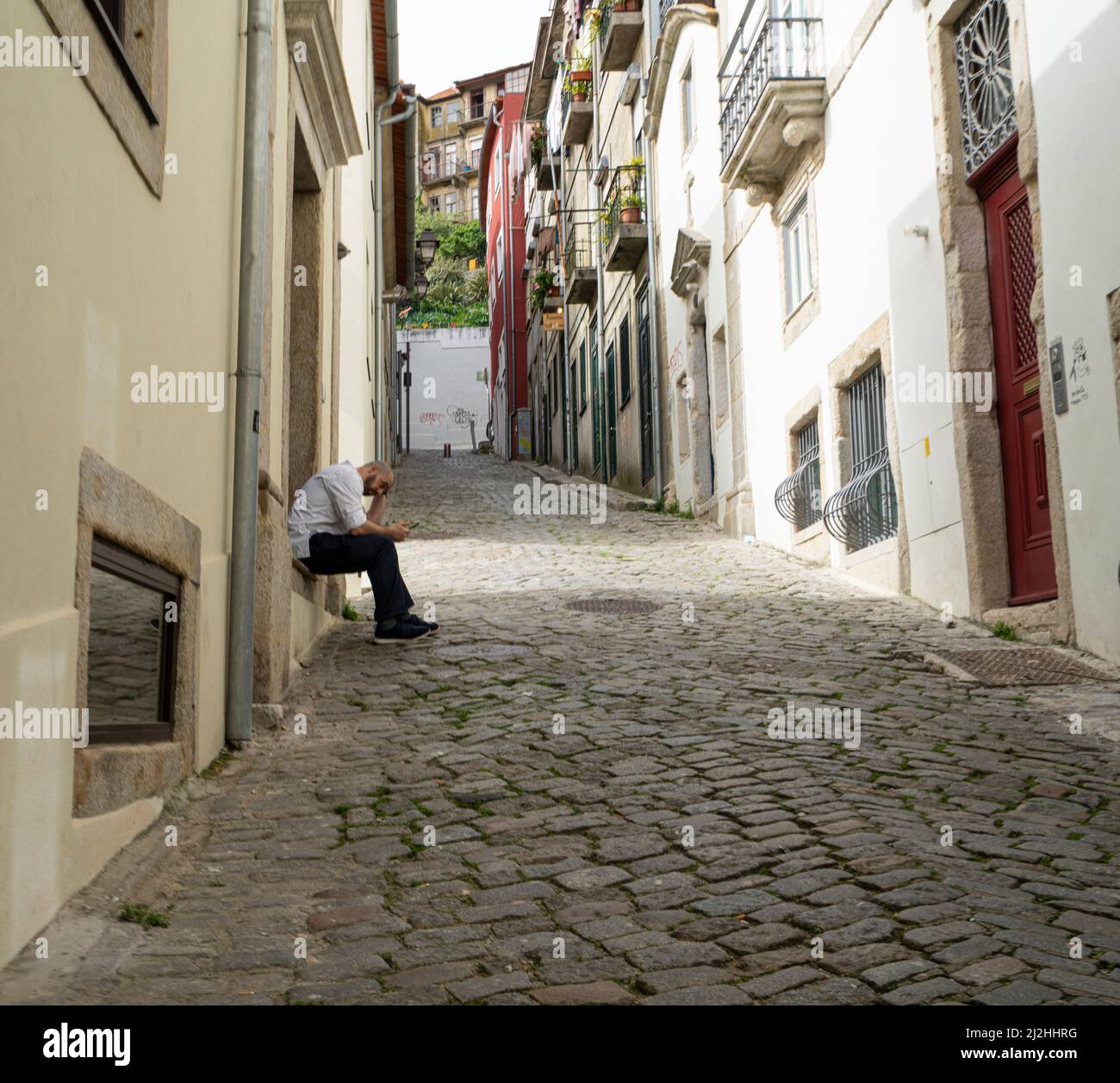 Porto, Portugal. March 2022. A man rests sitting on the step of his ...