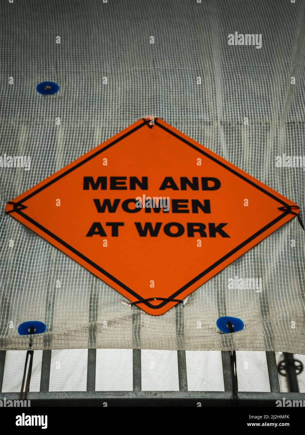 A vertical closeup shot of a red sign "Men and Women at work" inside a ...