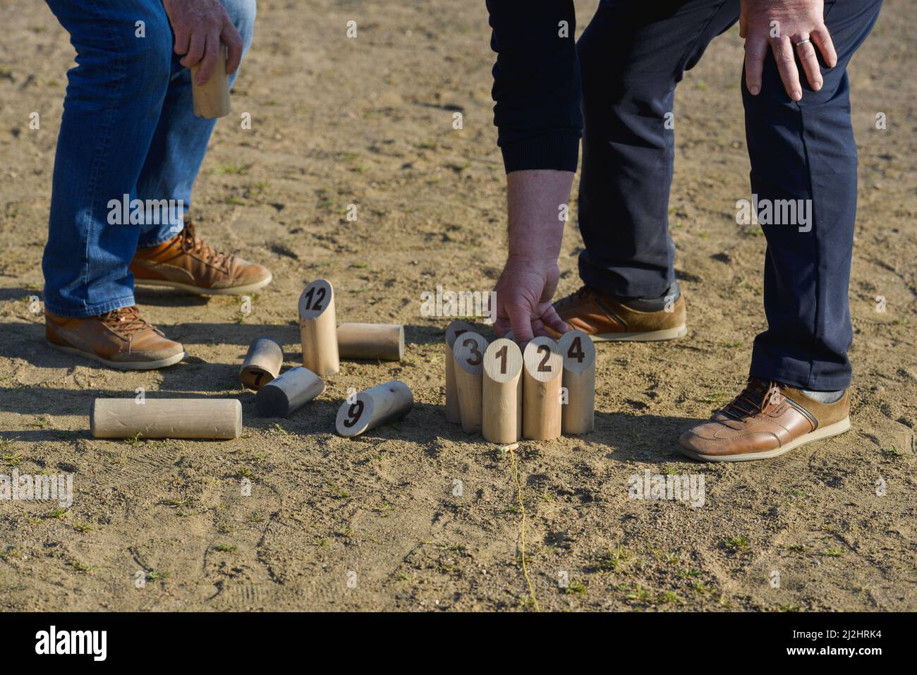 Two seniors putting back the skittles of the Molkky game on the sandy ...