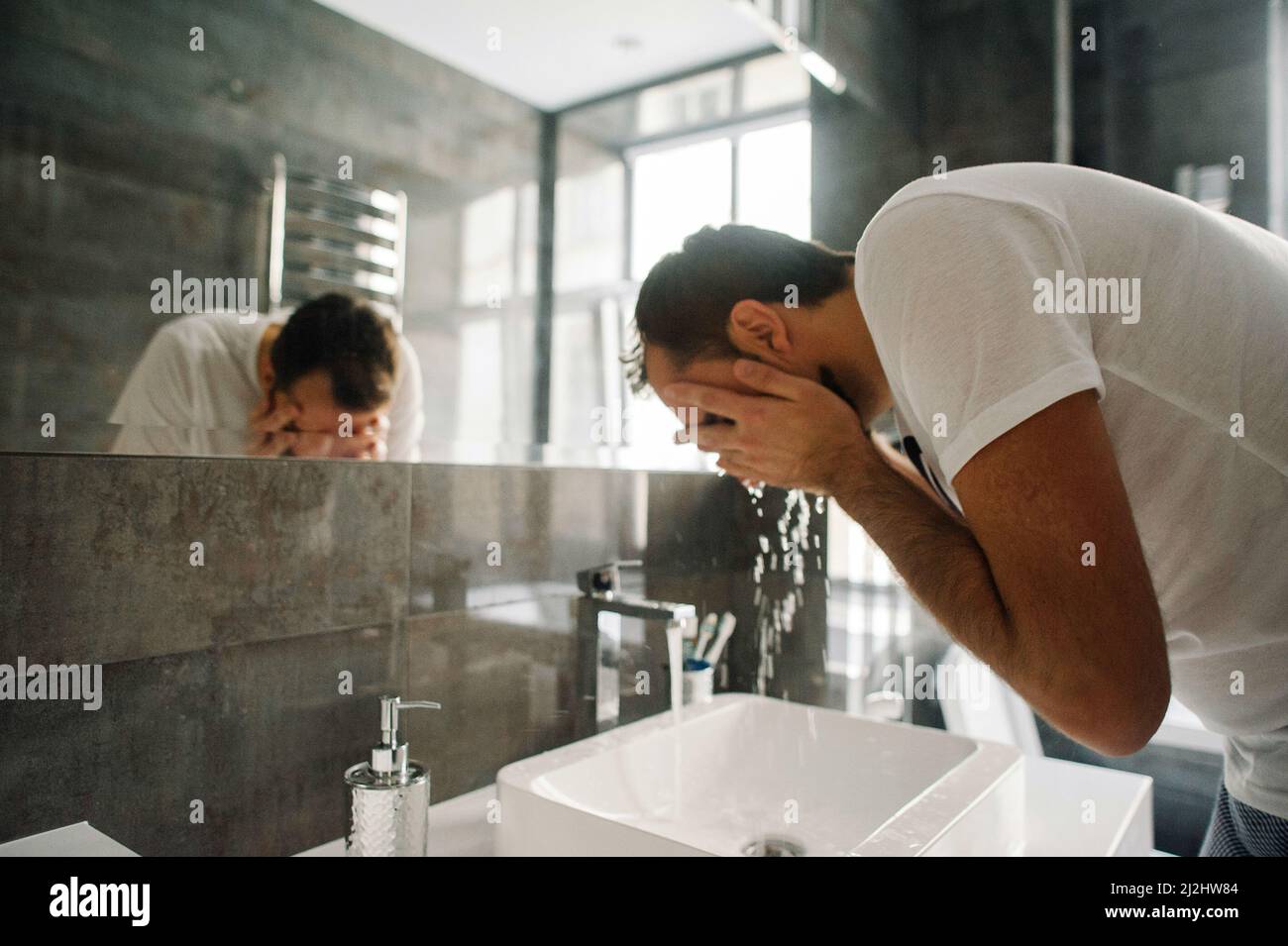 Brunette man in white T-shirt washing face in bathroom. Every day ...